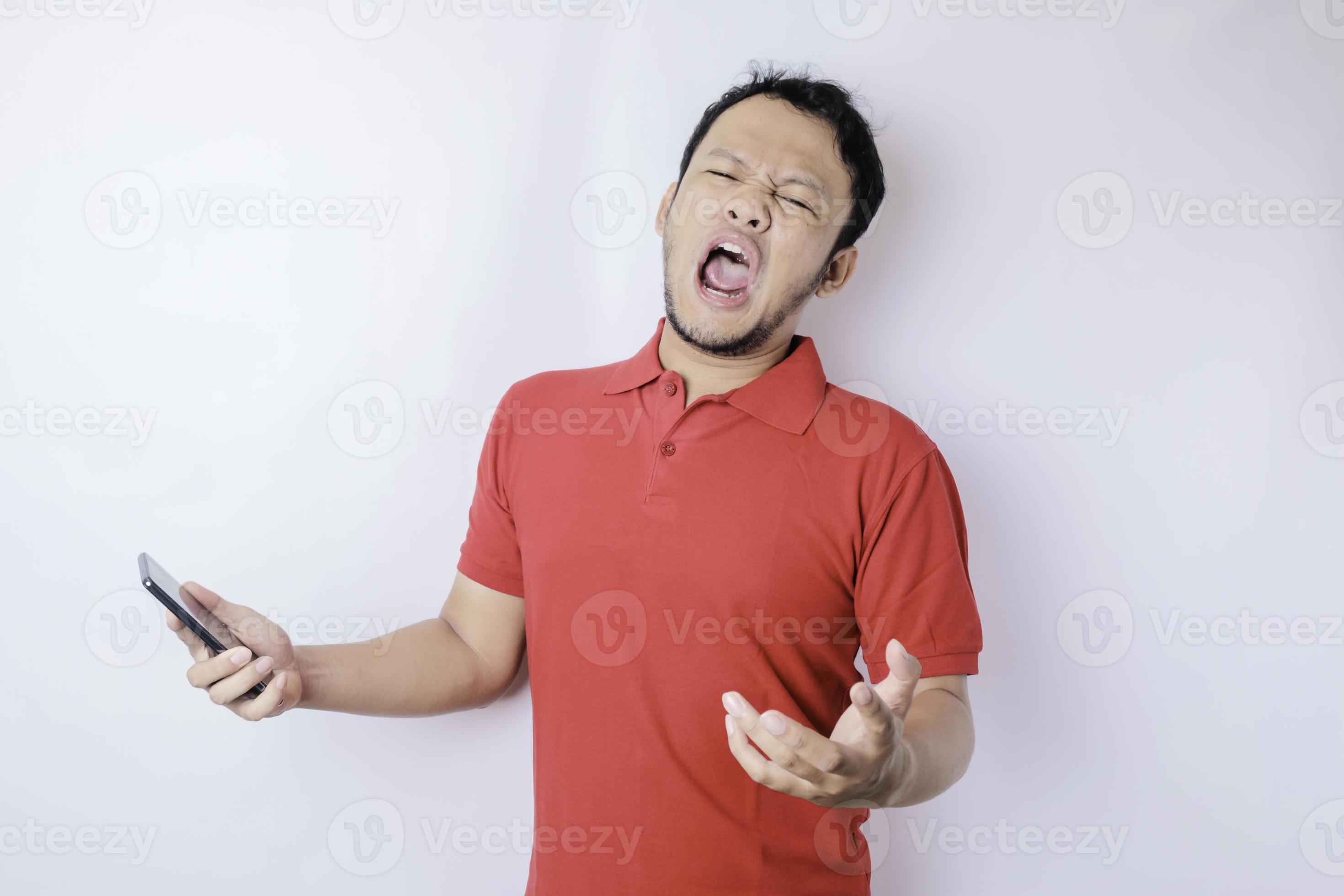 An angry young Asian man looks disgruntled wearing red shirt irritated face expressions holding ...