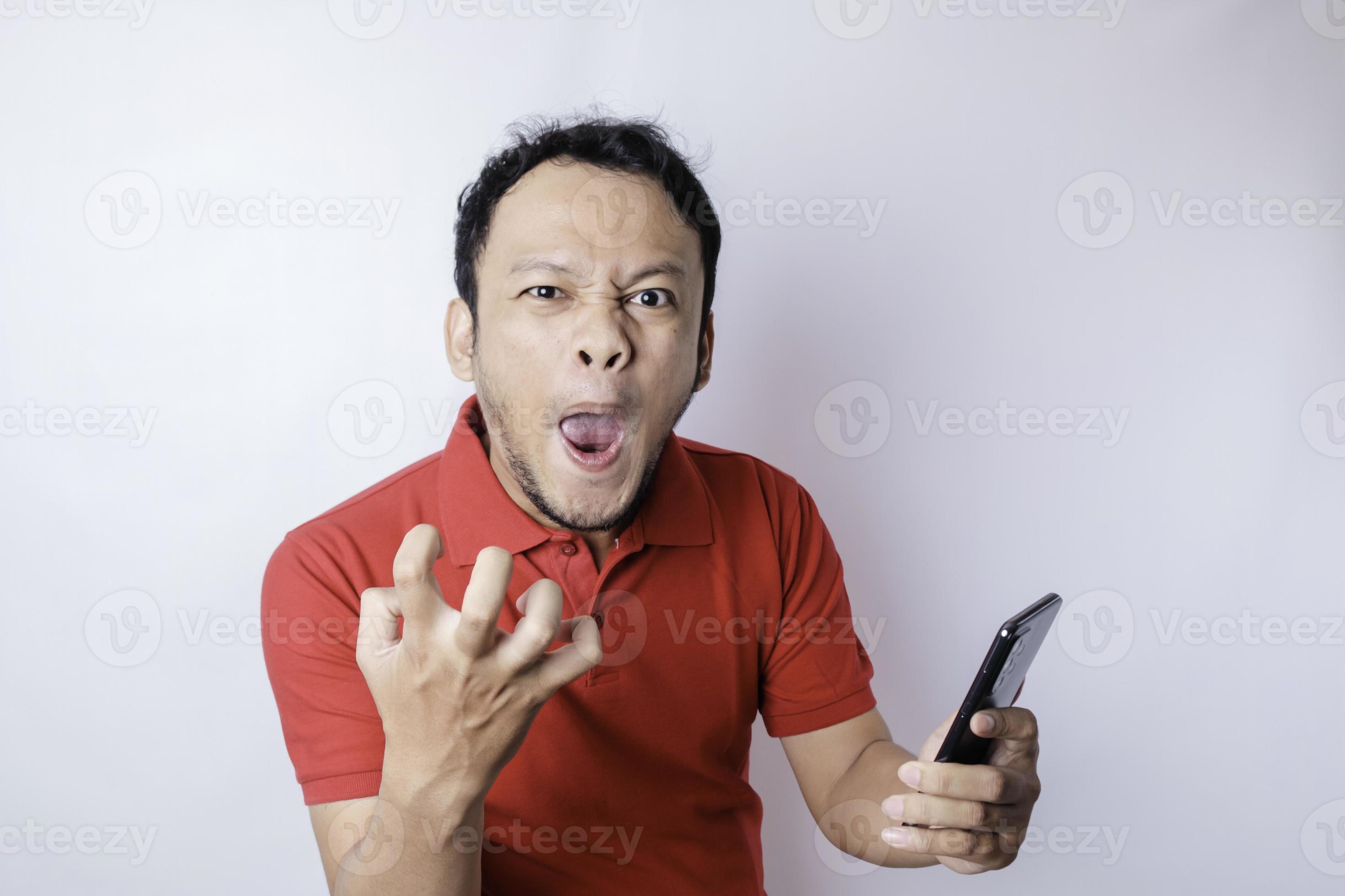 un joven asiático enojado se ve descontento usando una camisa roja con expresiones faciales ...