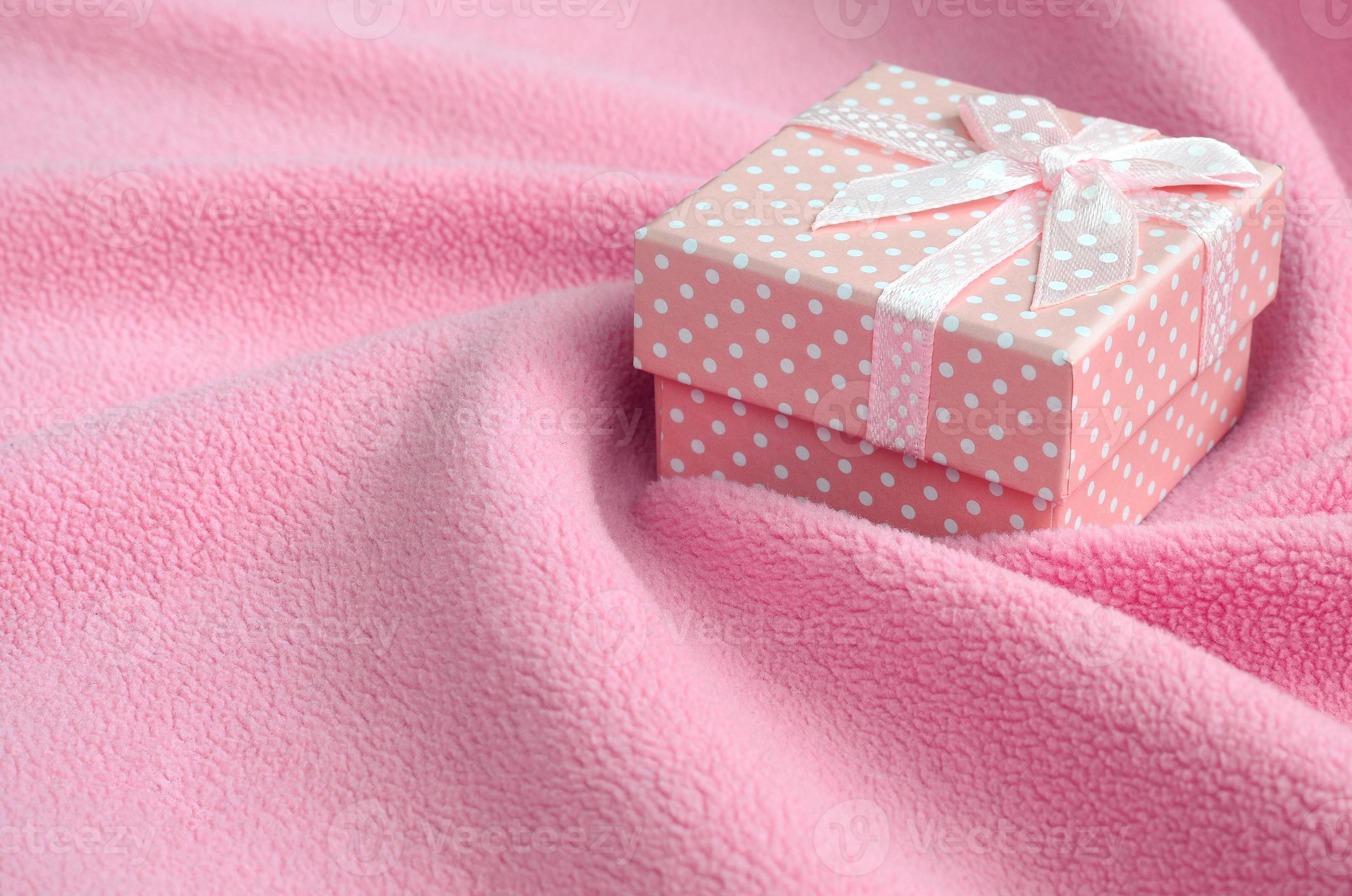 A small gift box in pink with a small bow lies on a blanket of soft and furry light pink fleece ...