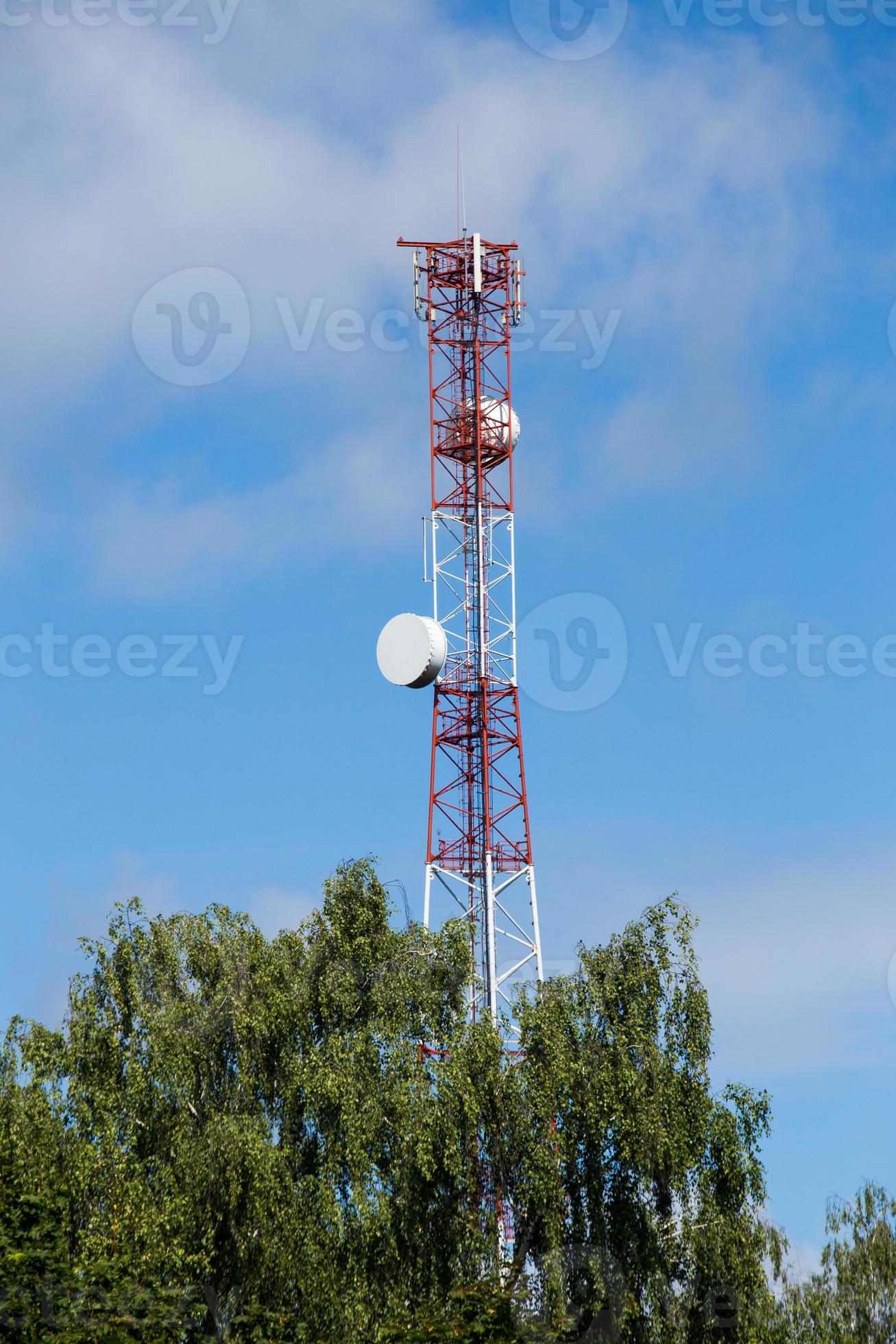 Red-white telecommunication tower with top of green tree on blue sky with clouds background ...
