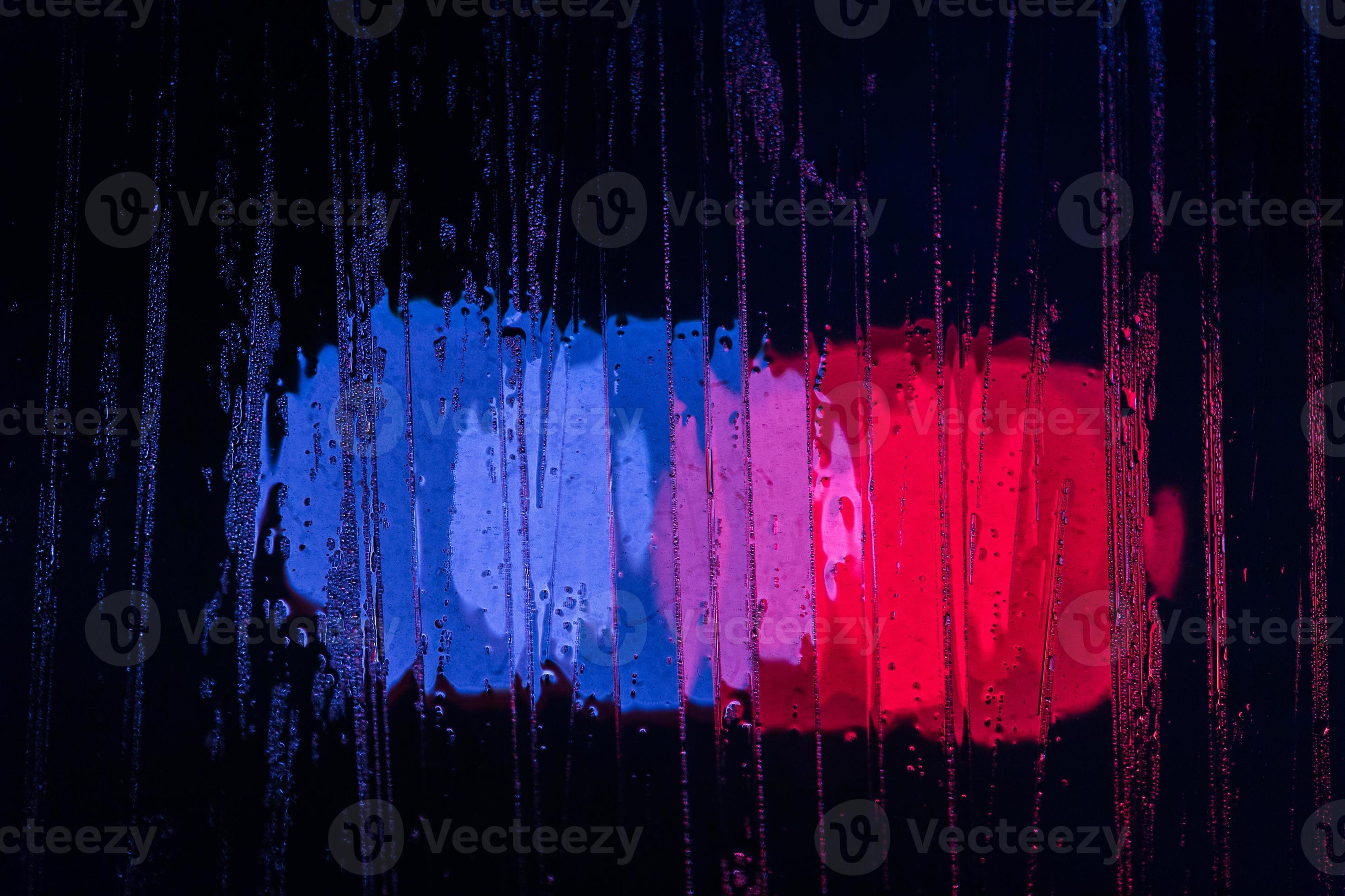 an abstract background of police lights bokeh trough wet glass at night close-up with selective ...