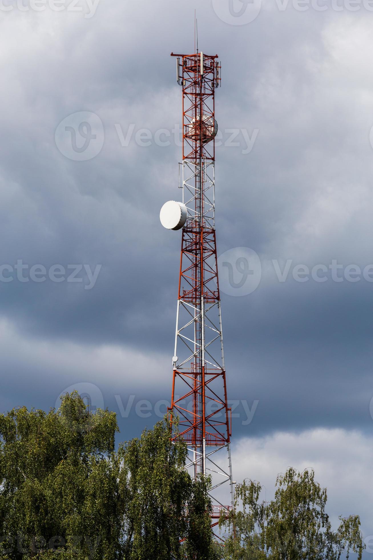 Red-white telecommunication tower with top of green tree on blue sky with clouds background ...