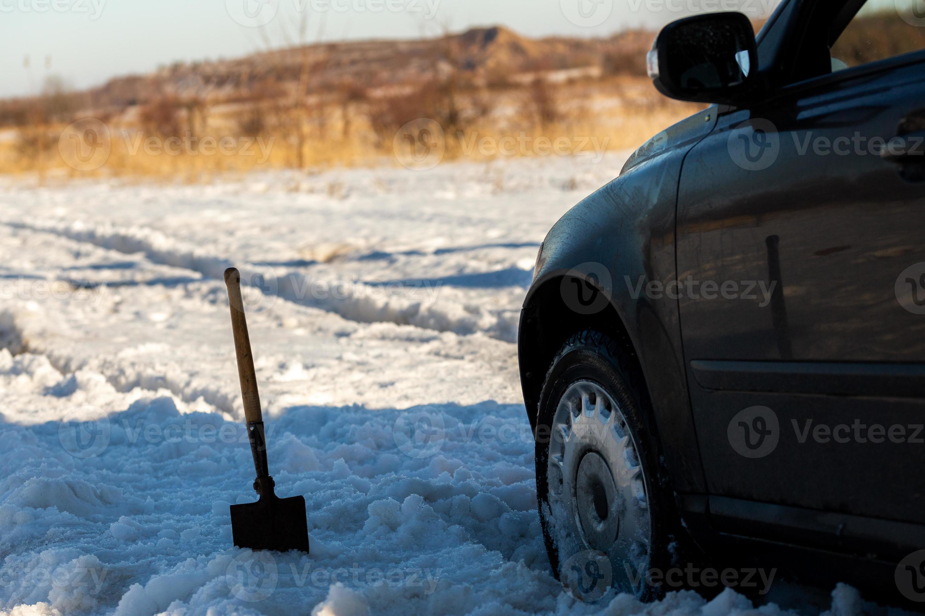 car stuck in snow offroad at daylight with shovel and selective focus ...
