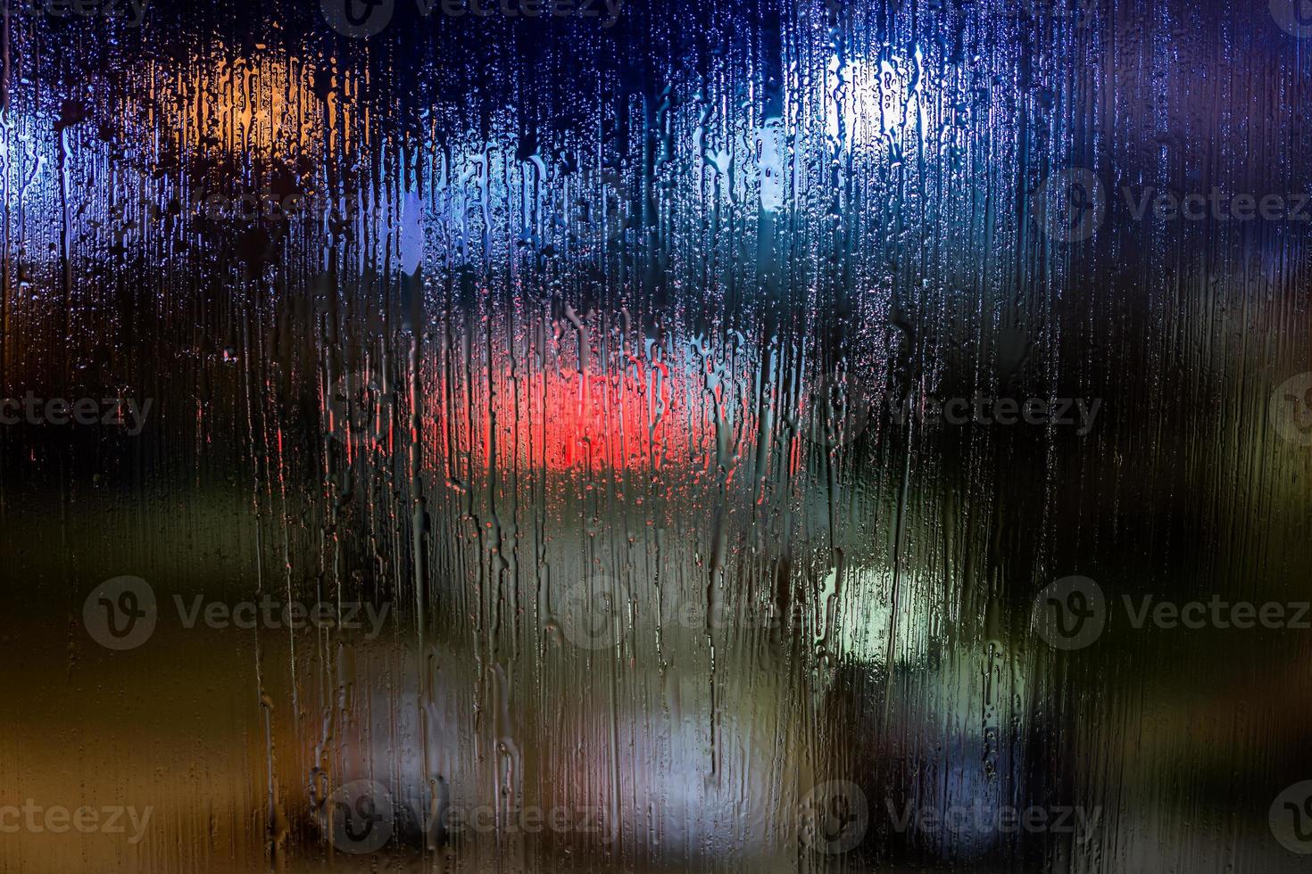 an abstract background night street lights bokeh through wet glass, close-up with selective ...