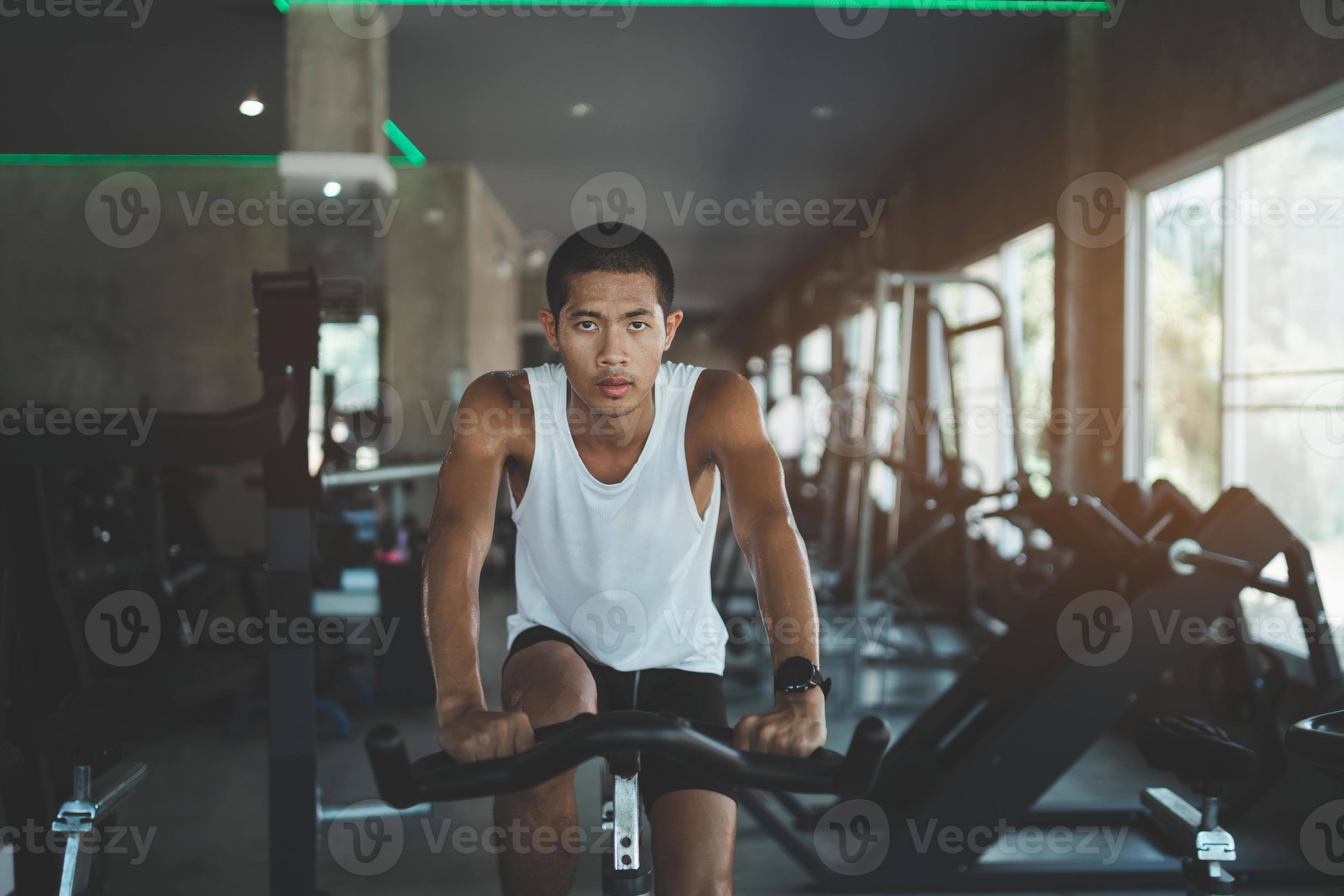 Asian sportsman exercising on a bicycle in the gym, determination to cardio lose weight, makes ...