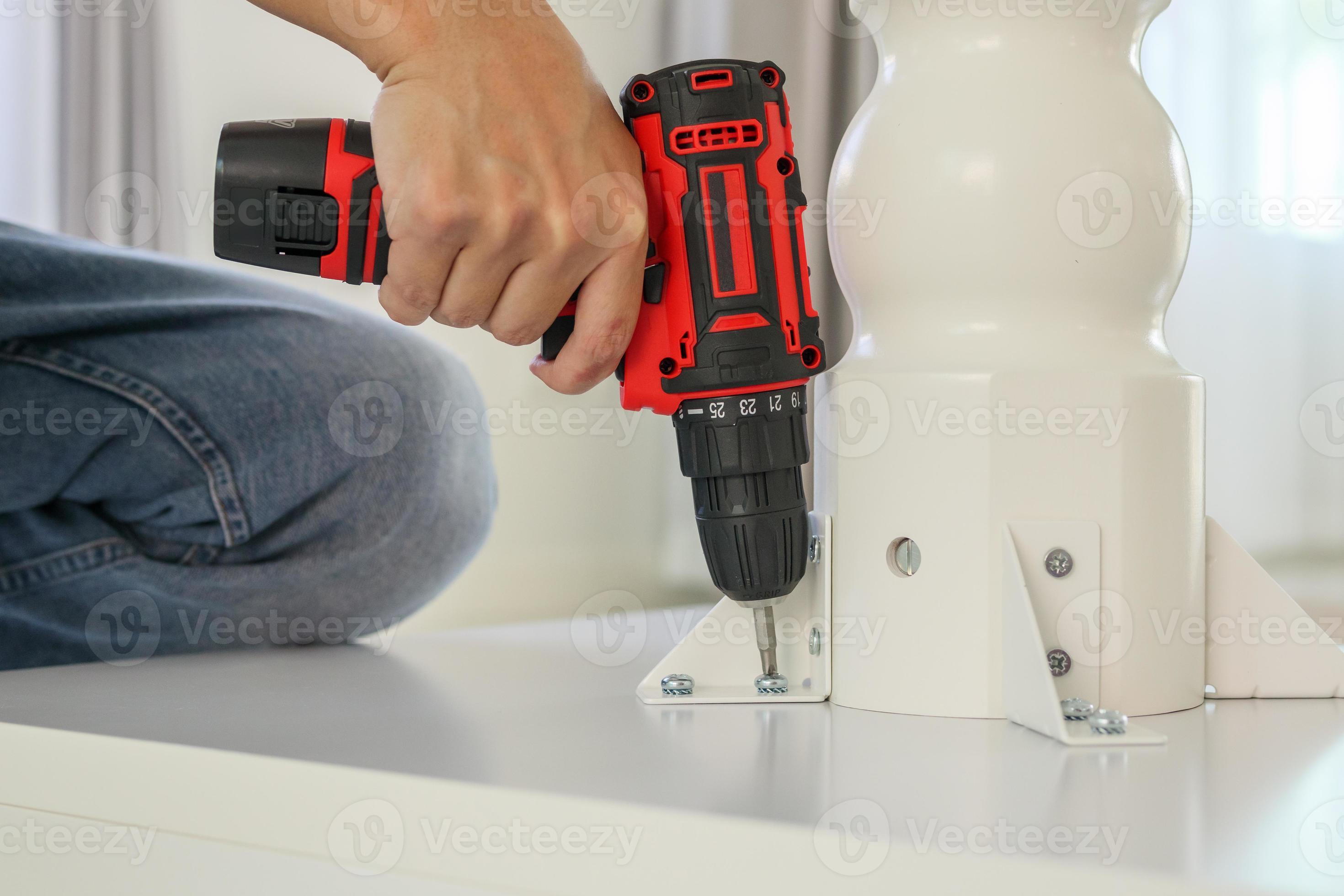 Man Assembling White Table Furniture At Home Using Cordless Screwdriver