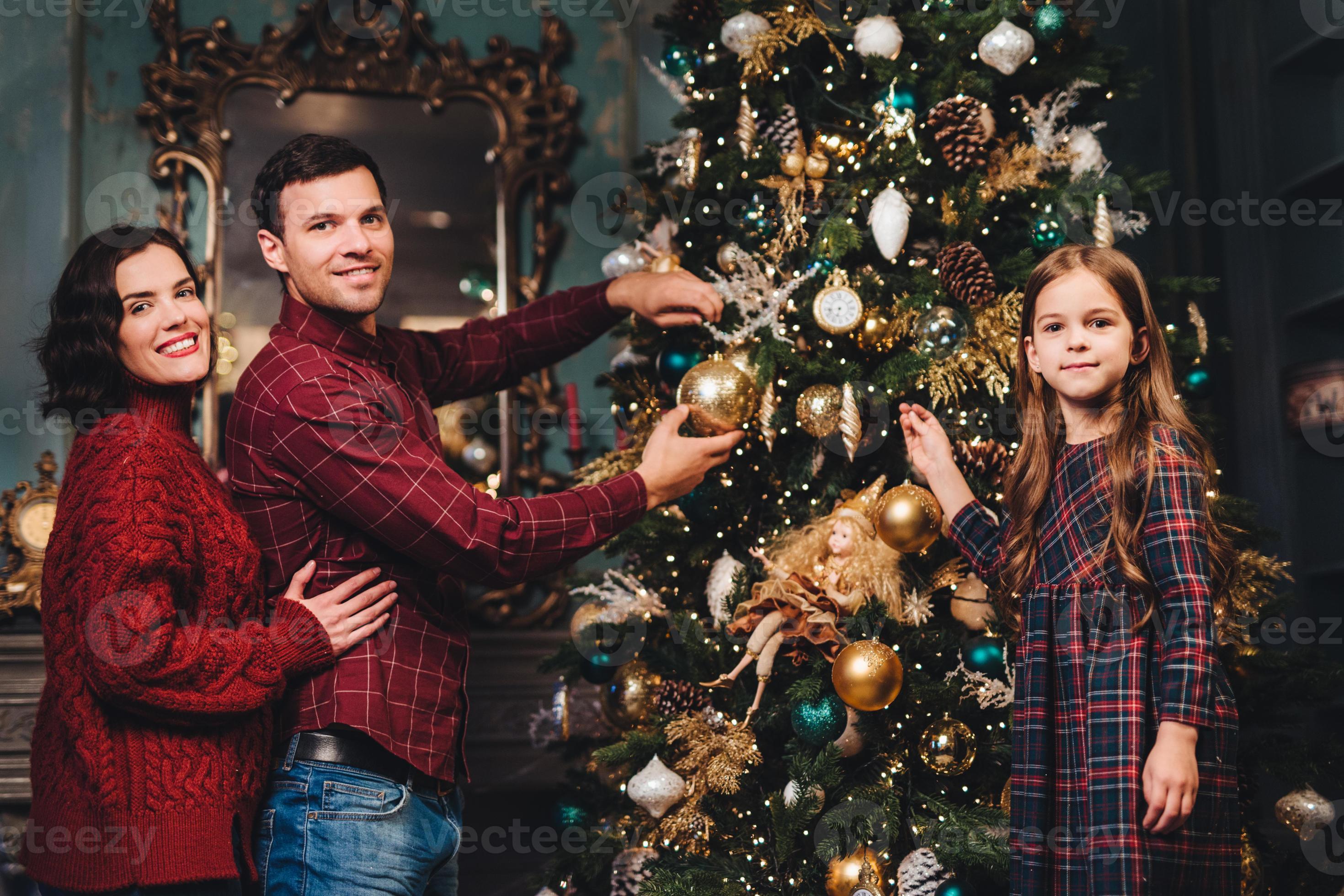 familia amistosa de padre, madre e hija decora el árbol de año nuevo, contentos de tener ...
