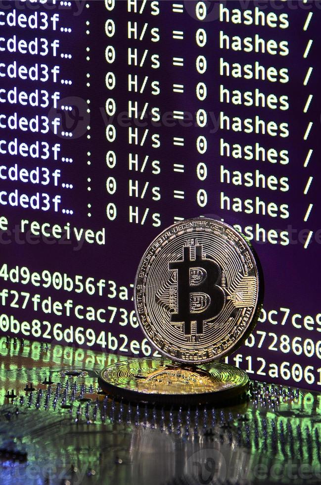 Two bitcoins lies on a videocard surface with background of screen display of cryptocurrency ...