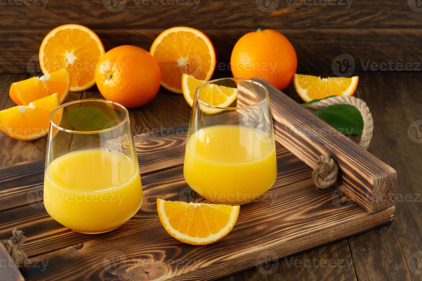 Fresh orange juice in glasses with cut oranges on wooden tray. Rustic still life with citrus ...