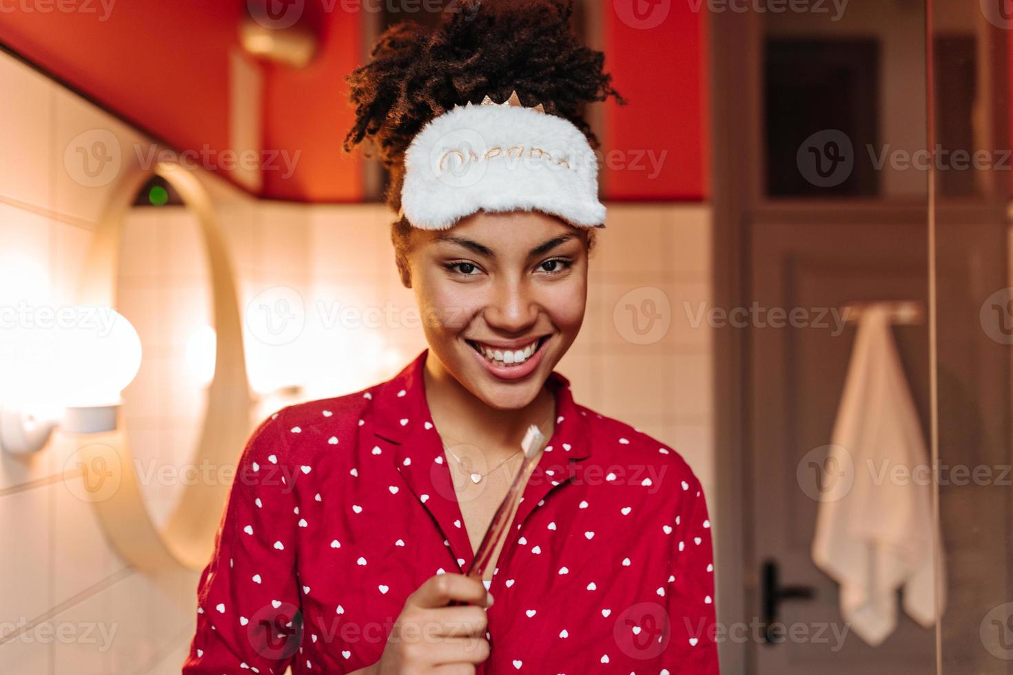 Young Girl With Smile Looks Into Camera And Holds Toothbrush On Background Of Bathroom Mirror