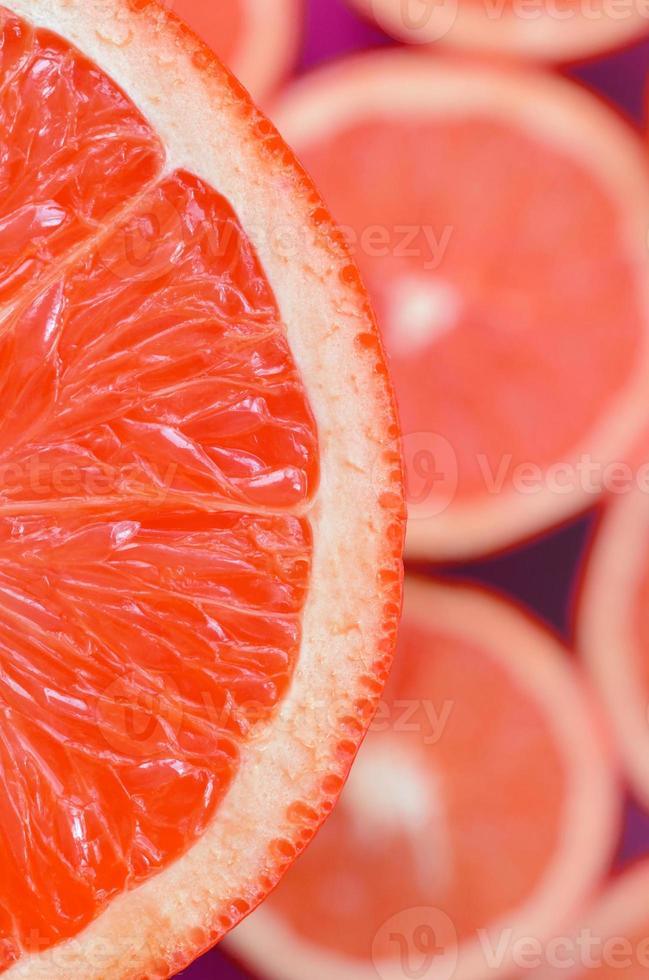 Top view of a fragment of the red grapefruit slice on the background of many blurred grapefruit ...
