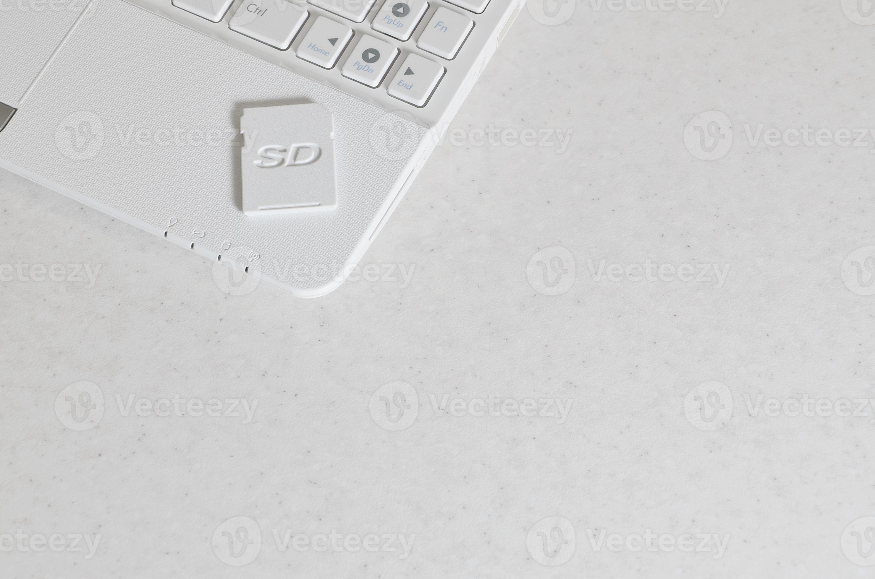 A compact SD memory card lies on a white netbook. The digital information storage device is ...