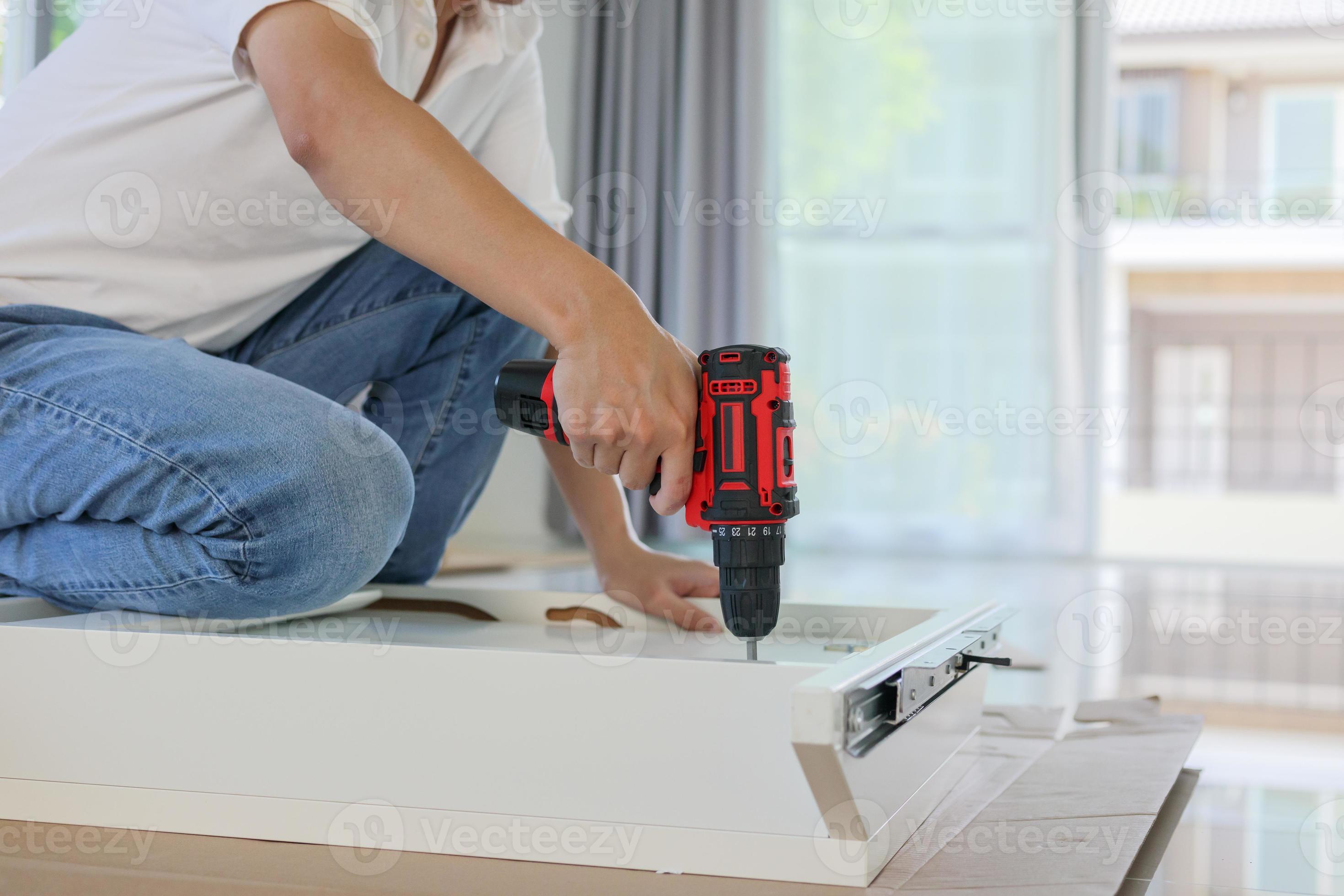Man Assembling White Table Furniture At Home Using Cordless Screwdriver