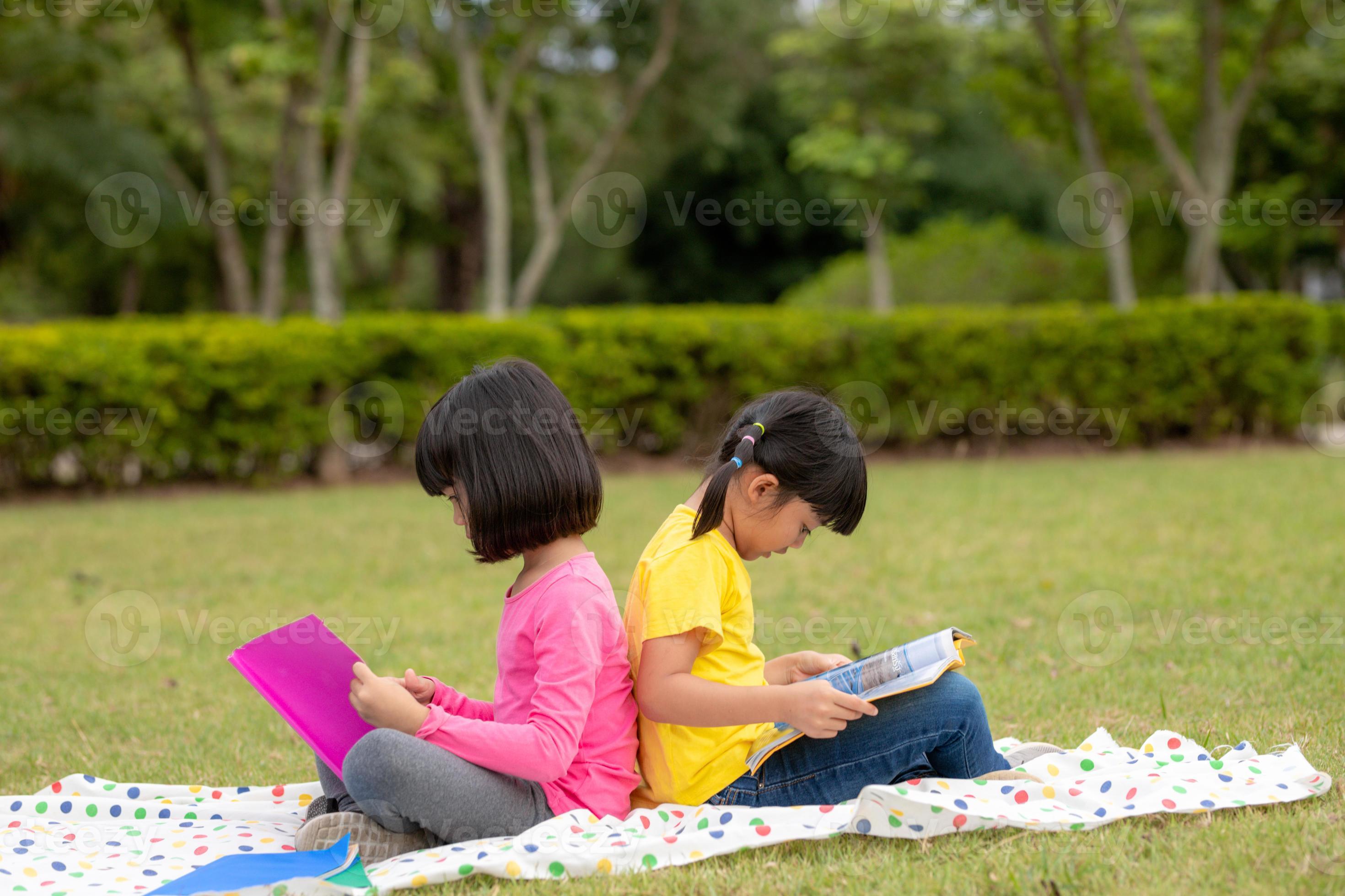 two beautiful little girls reading books in the garden , sitting on grass. The concept of ...