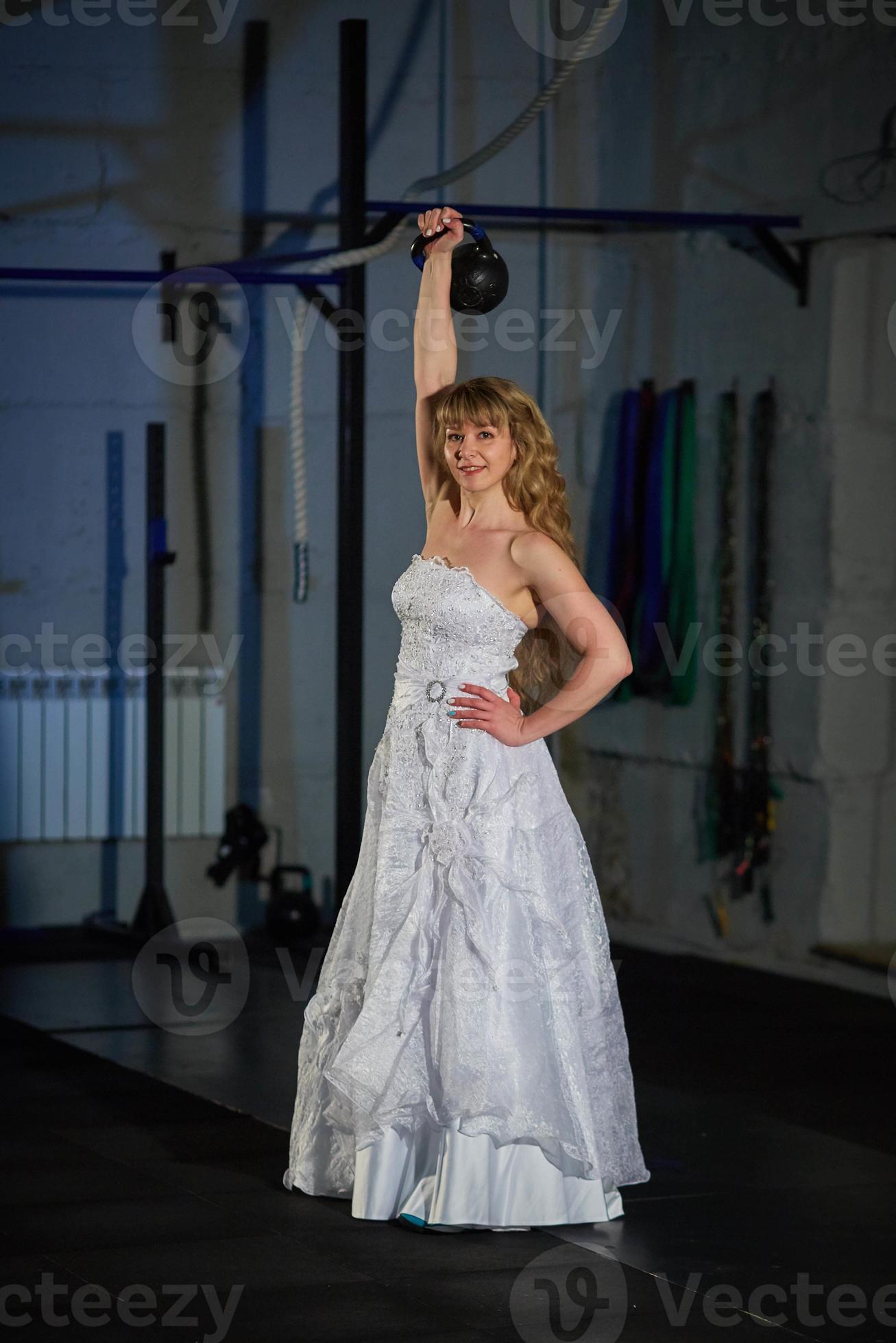 novia musculosa en vestido de novia haciendo ejercicios con un gran peso en el gimnasio. buena ...