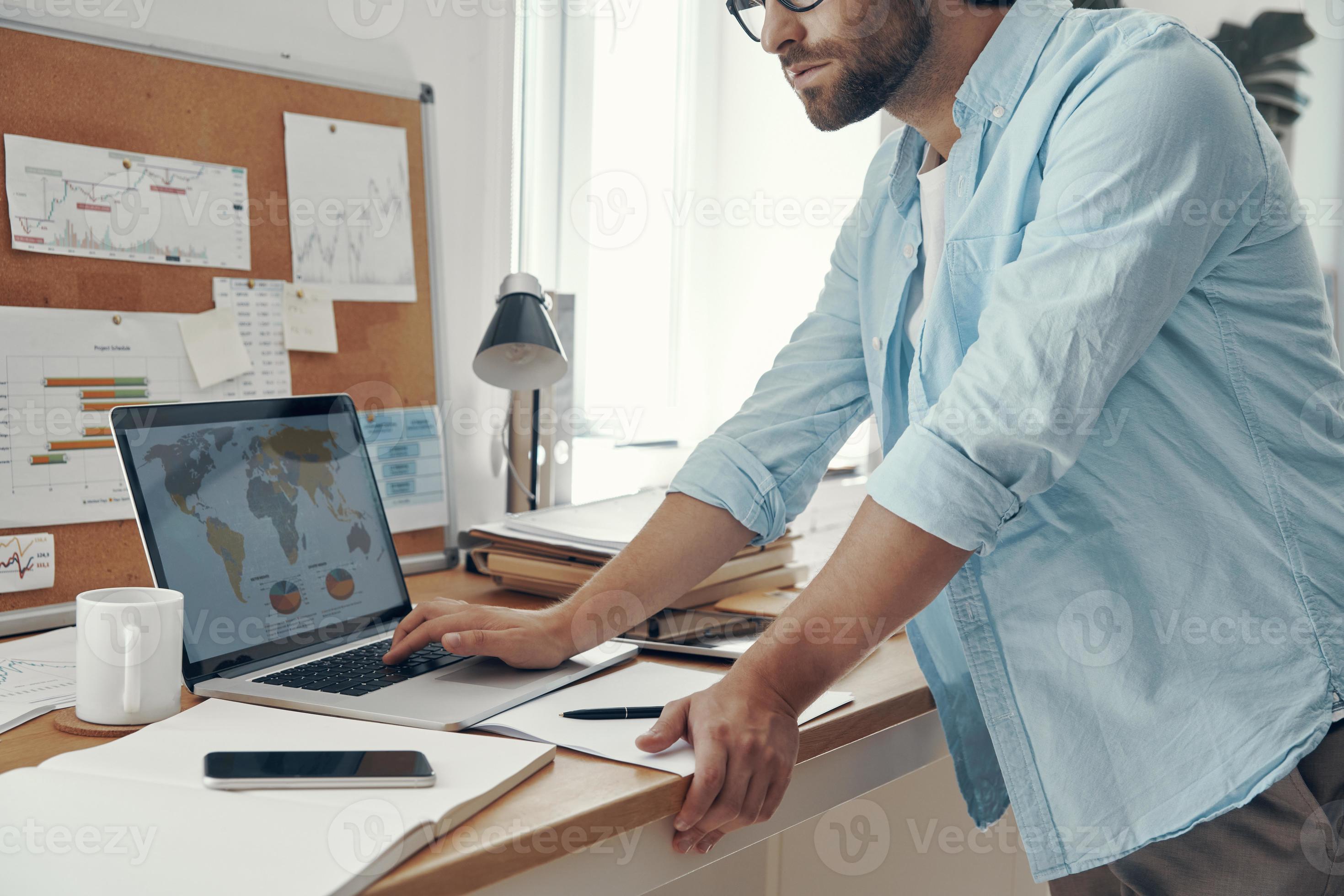 Close-up of young man working on laptop while standing near his working ...