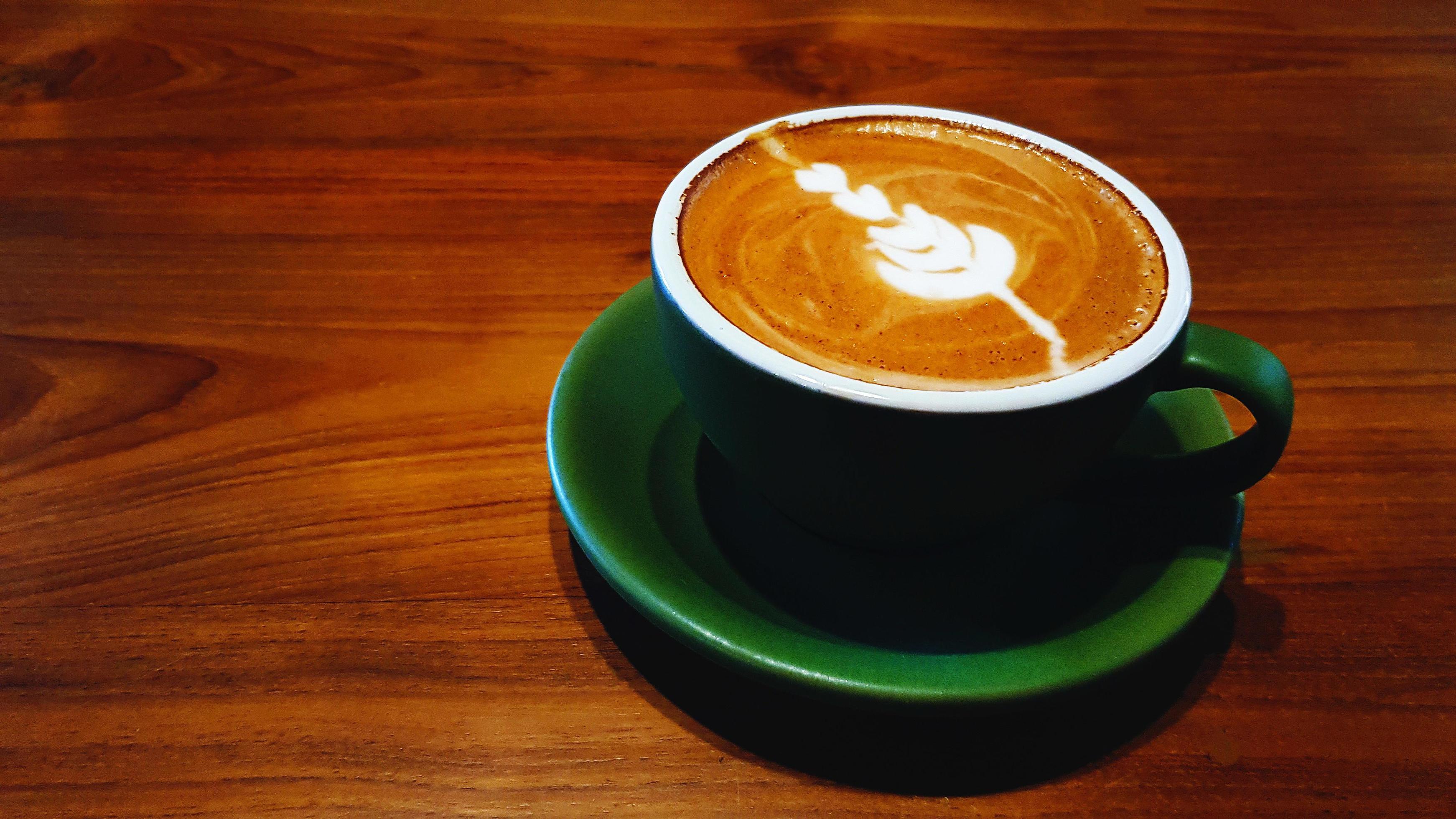 Cup of art cappuccino or latte coffee on brown wooden background. Hot drinking in green glass at ...
