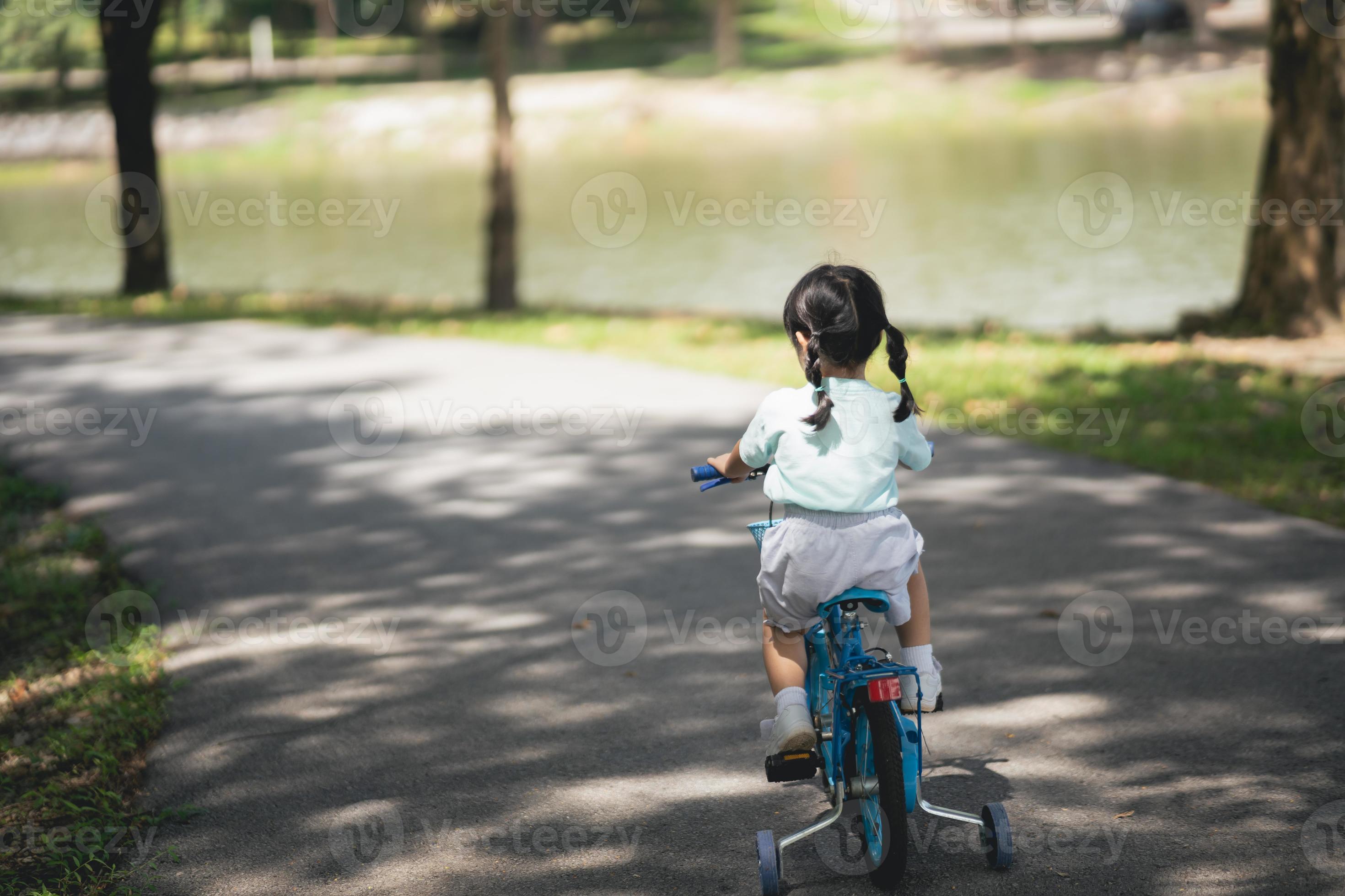 Back side view of asian baby girl child learning to ride bicycle in the park garden. Education ...