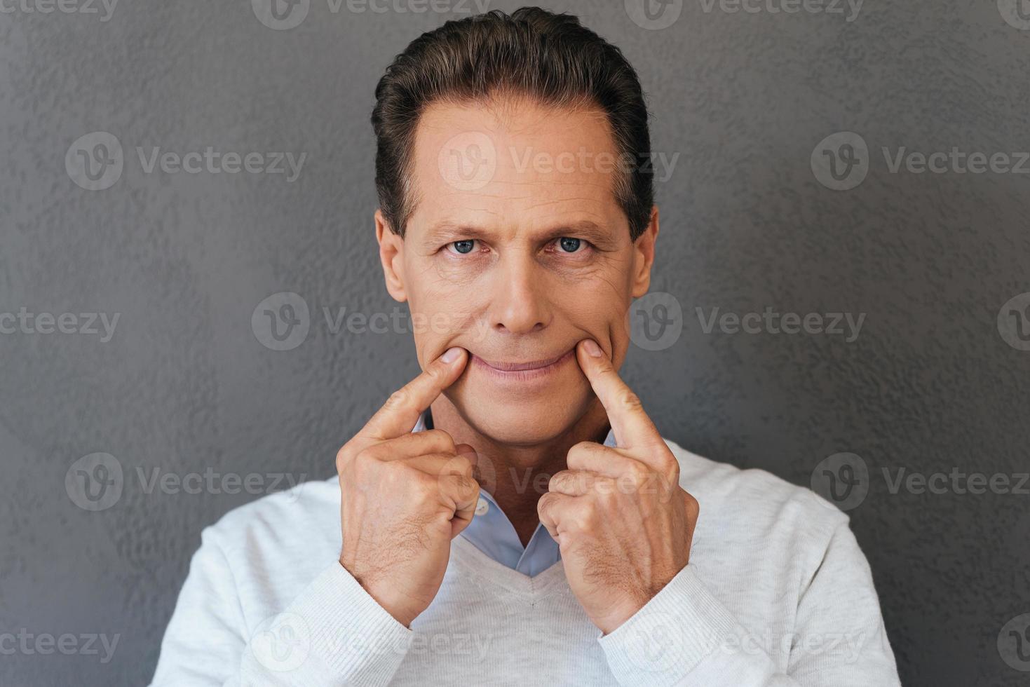 Forced Smile Mature Man Making Forced Smile While Standing Against Grey Background 13487789