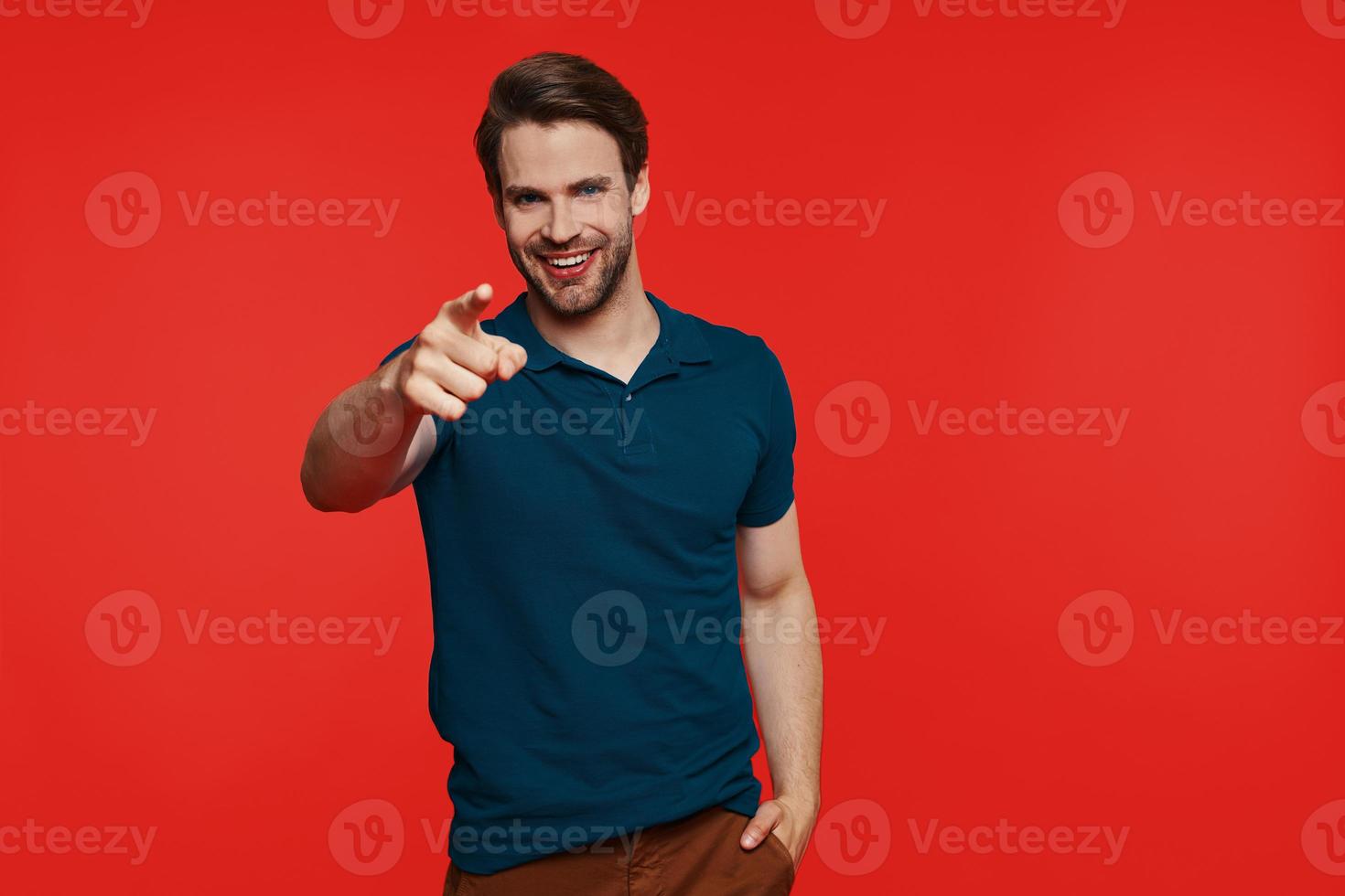 Happy young man in casual wear pointing camera while standing against ...