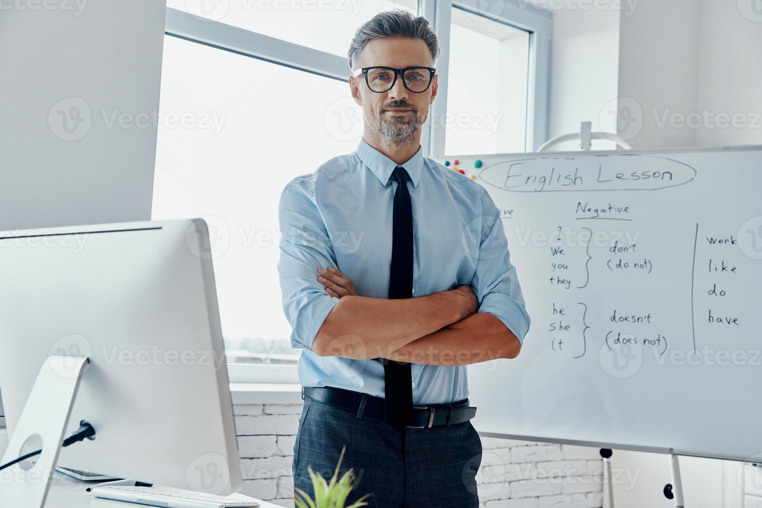 Confident English teacher looking at camera while standing near the ... Confident English teacher looking at camera while standing near the ...