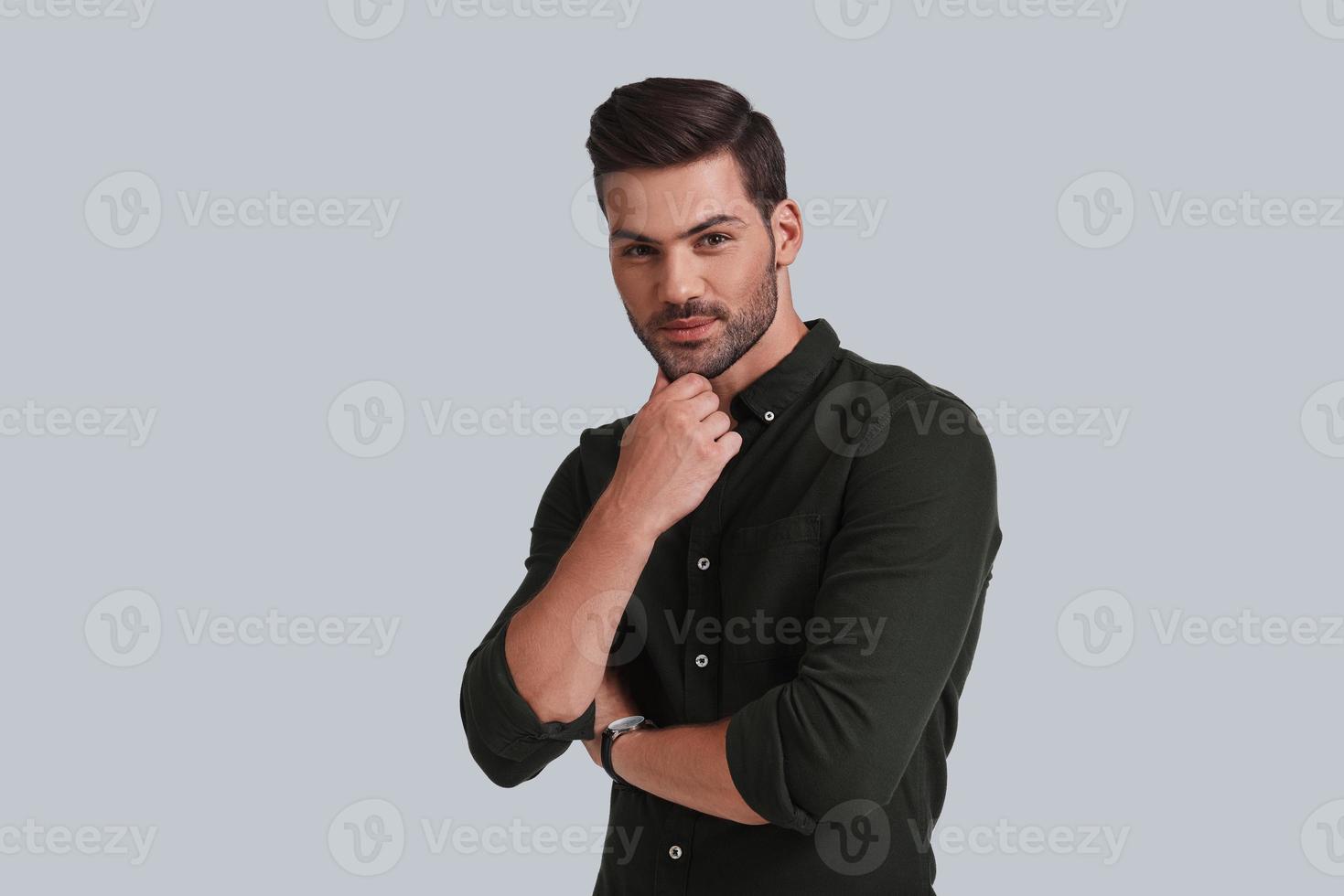 Totally perfect. Handsome young man keeping hand on chin and looking at ...