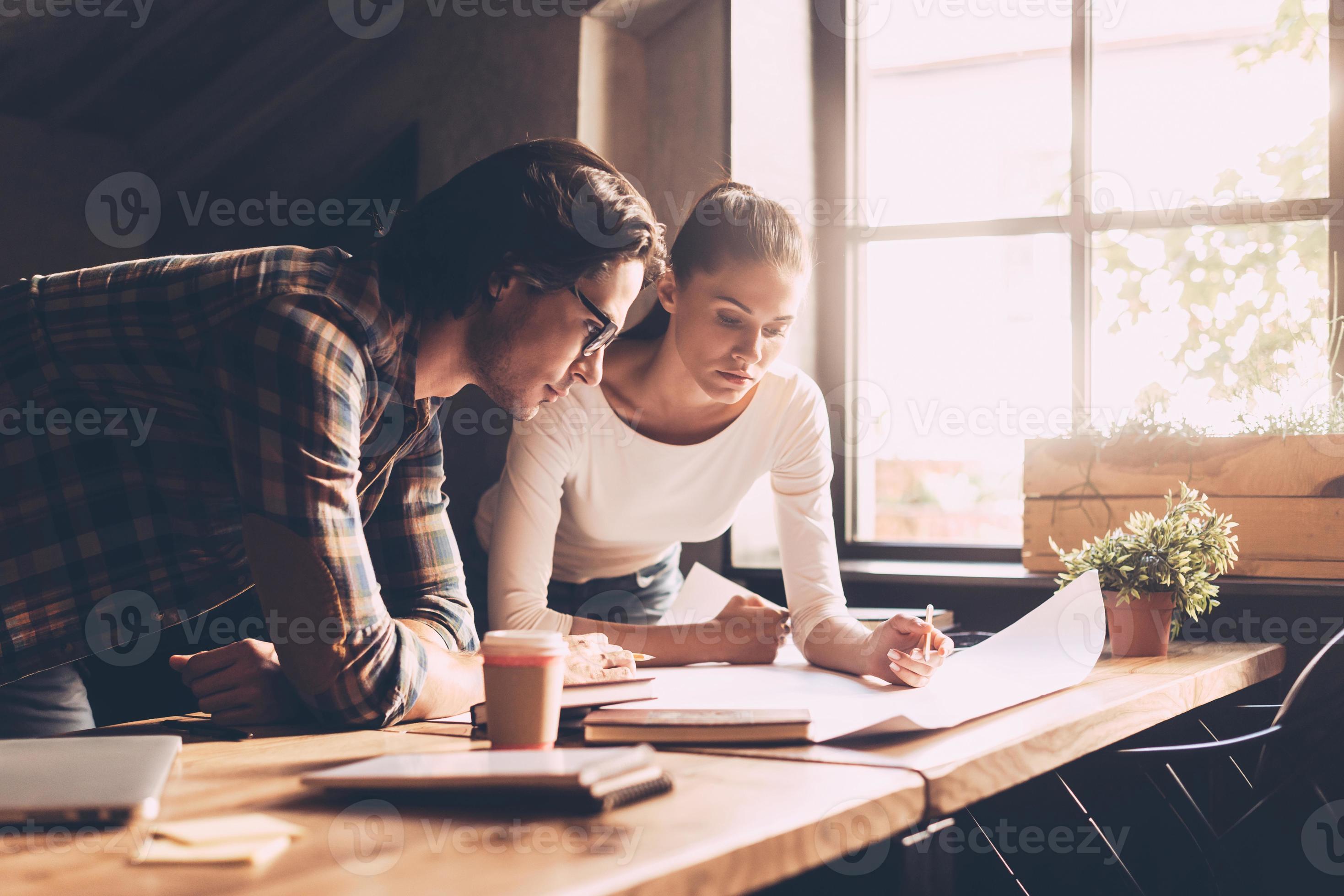 Finding solution together. Confident young man and woman in casual wear looking at blueprint ...