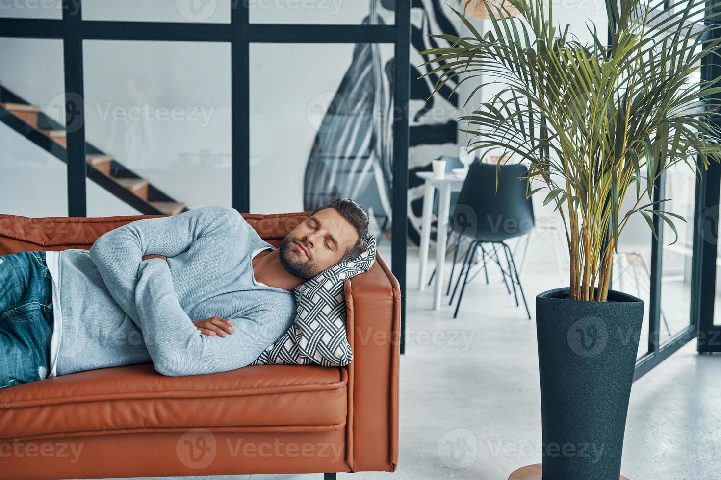 Handsome young man in casual clothing sleeping on the sofa at home ...