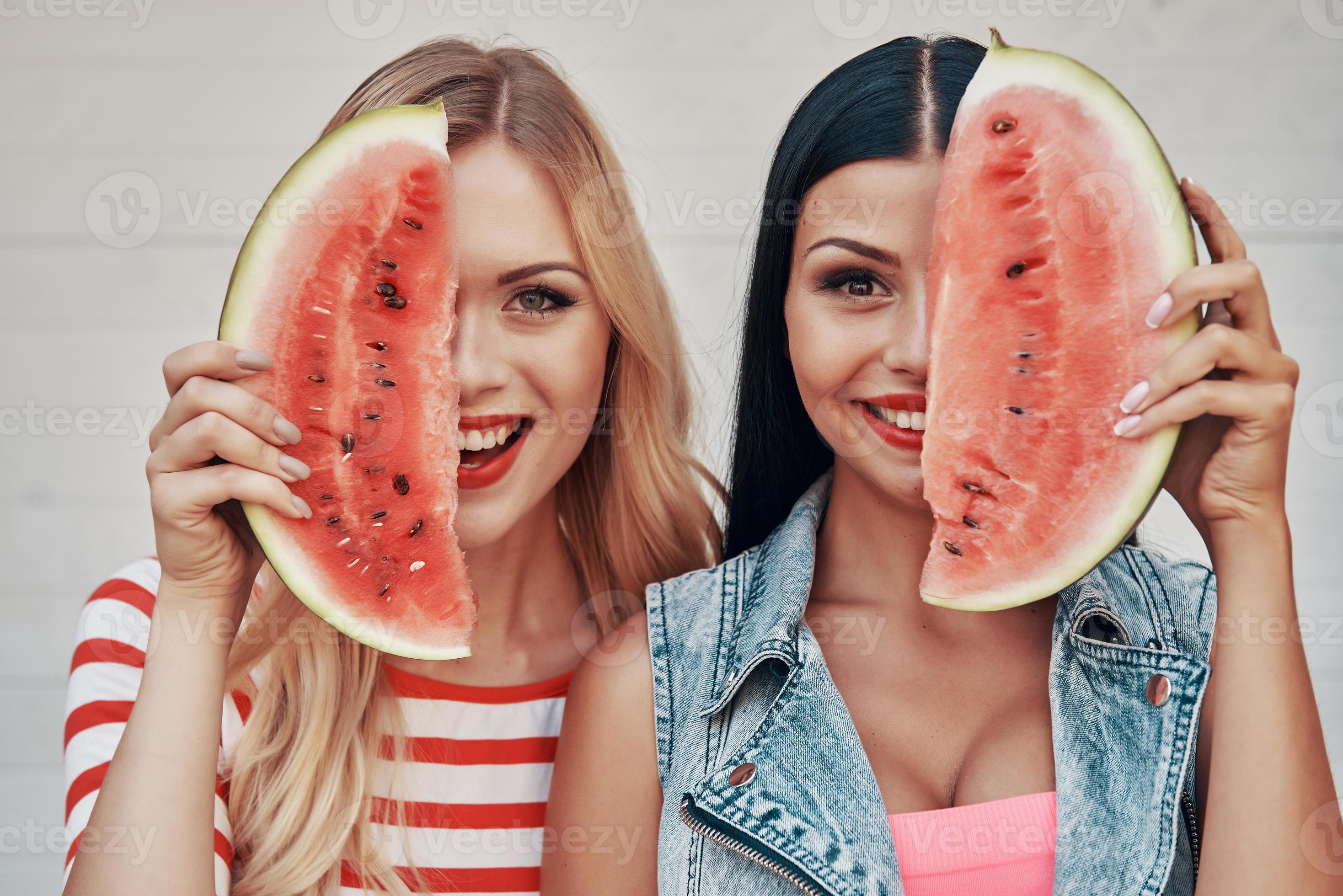 Summer is time for fun. Two playful young women holding slices of watermelon against half part ...
