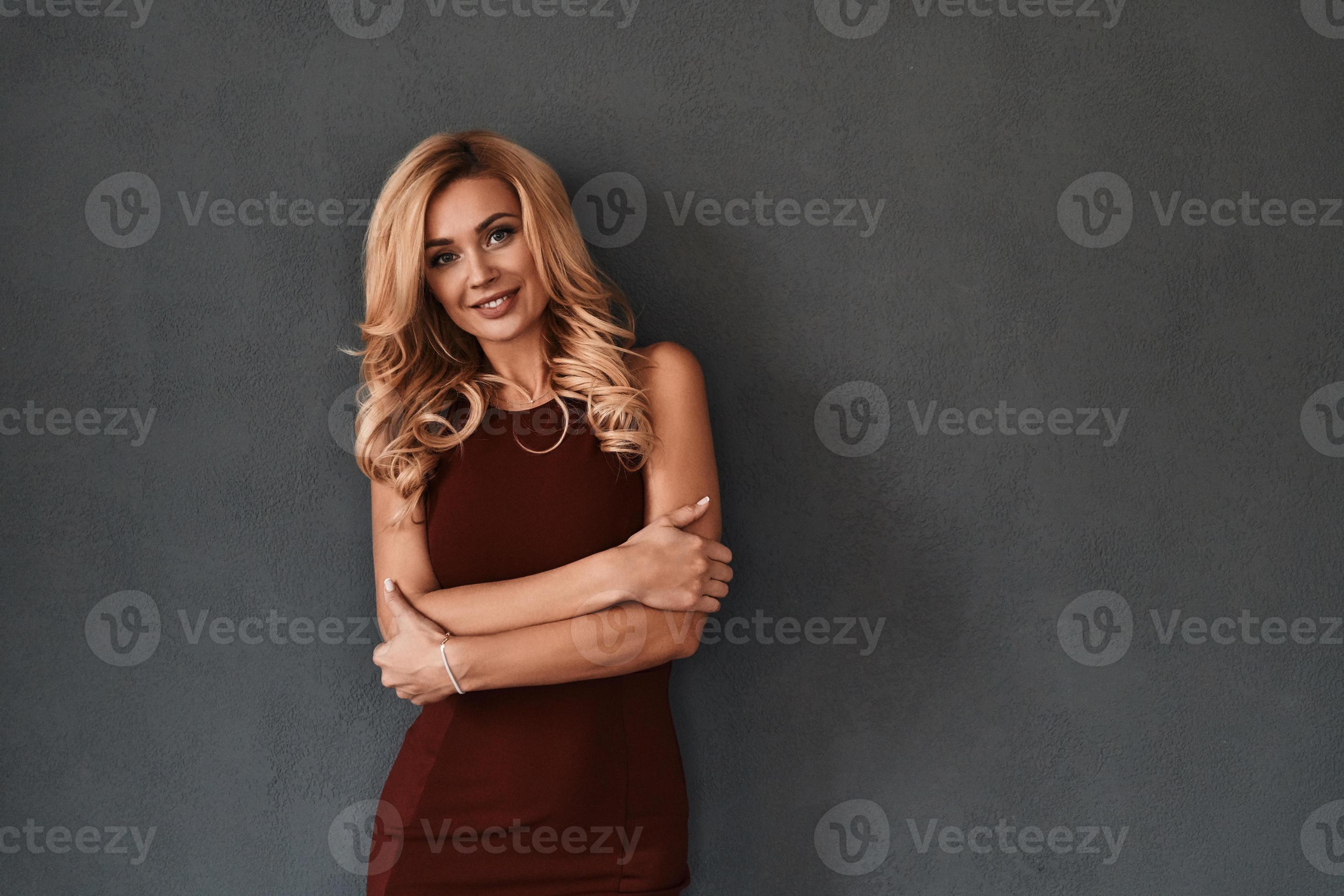 Sincere smile. Attractive young woman in dress keeping arms crossed and ...
