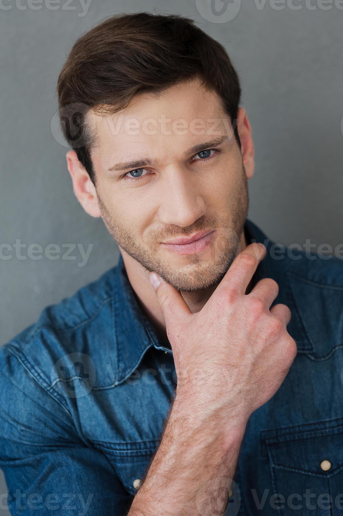 Casually handsome. Handsome young man holding hand on chin and looking ...