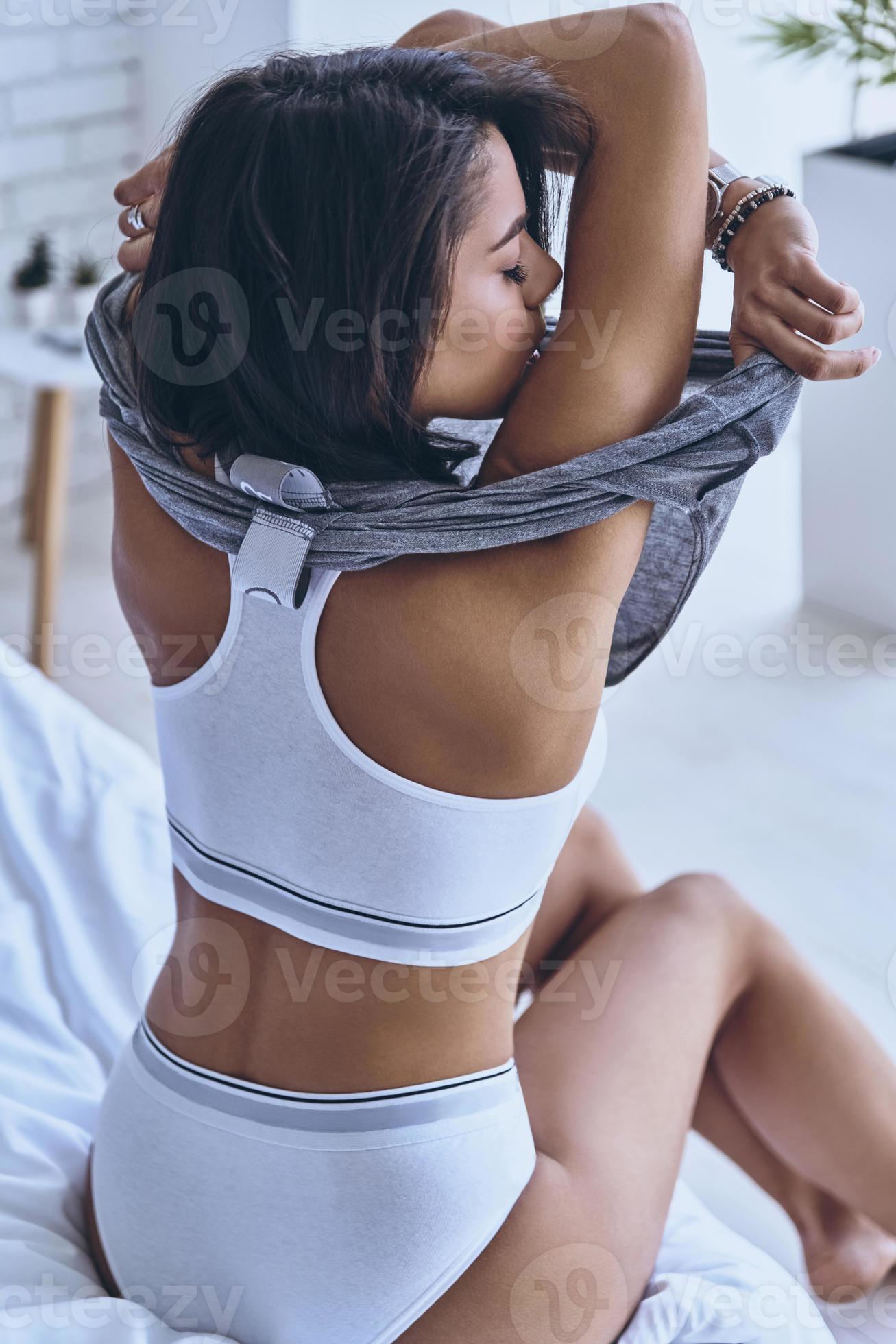 Taking it off. Rear view of attractive young woman in underwear taking ... Taking it off. Rear view of attractive young woman in underwear taking ...