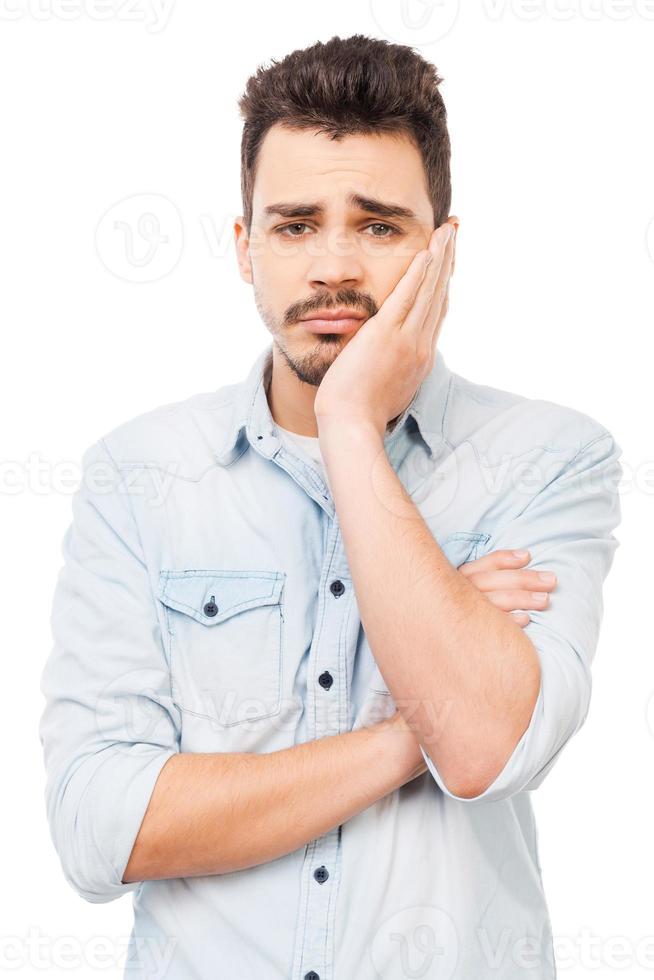 Feeling bored. Frustrated young man in shirt holding hand on his cheek ...