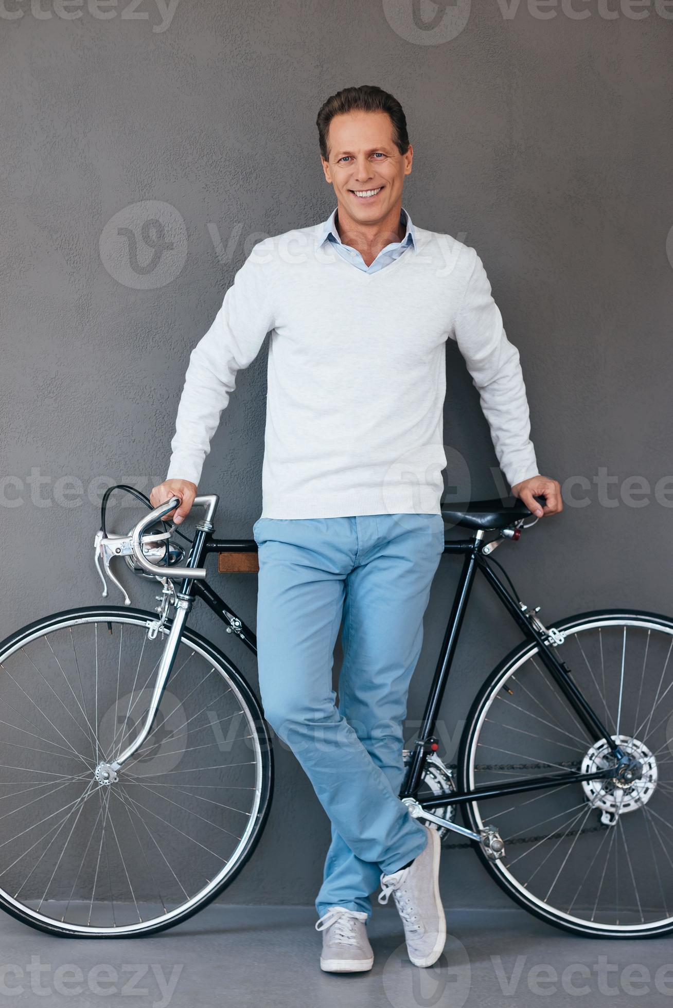 I love my bike Confident mature man leaning at his bicycle and smiling while standing against ...