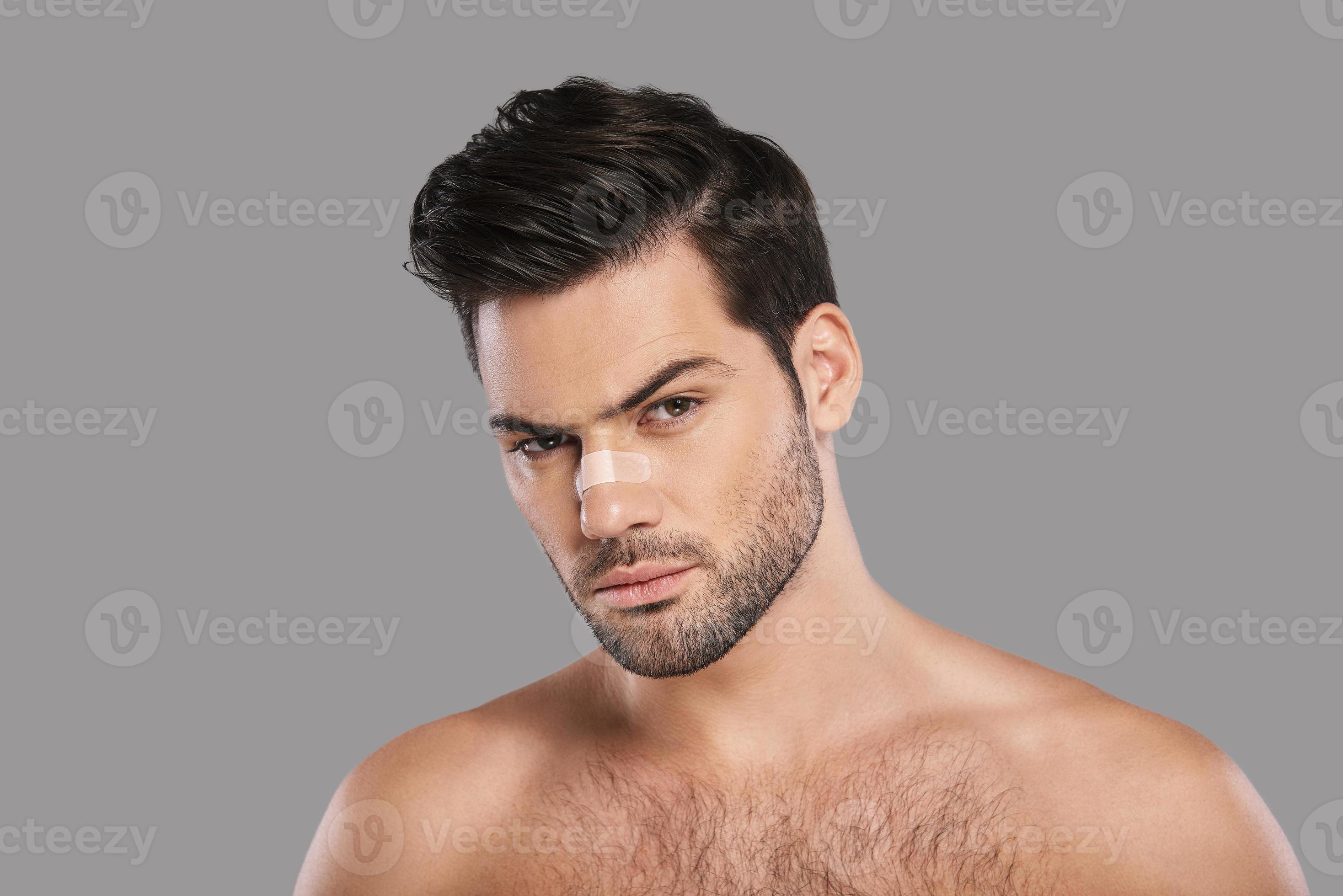 Real man. Handsome young man with adhesive bandage on his nose looking at camera while standing ...