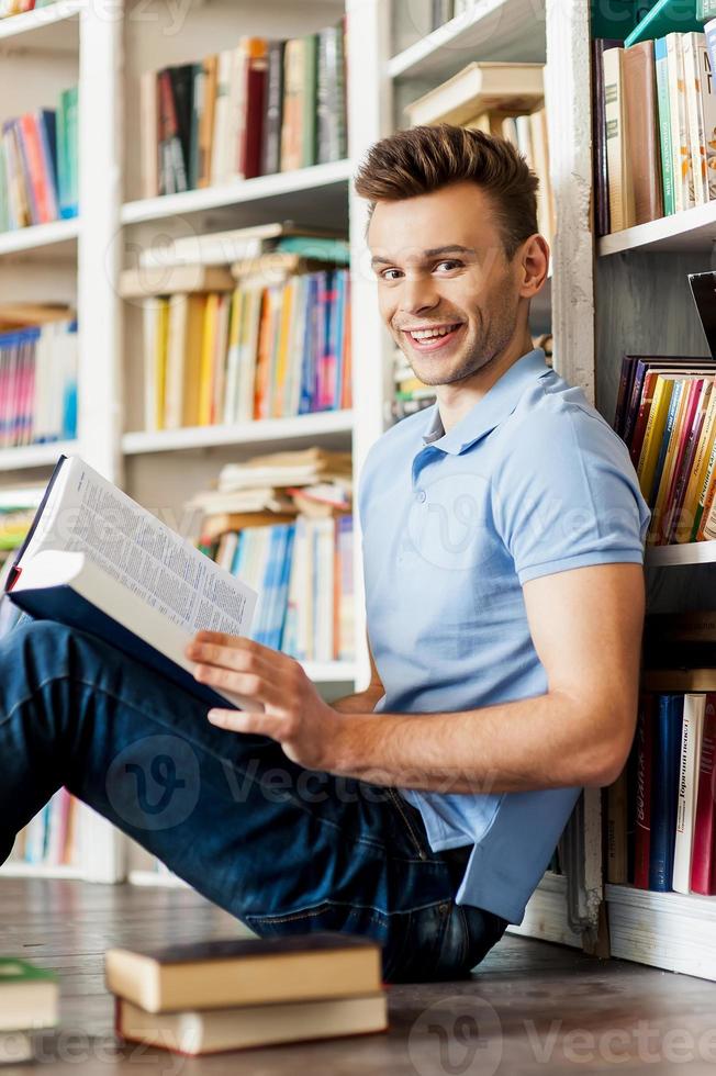 Student in library. Side view of handsome young man holding a book and ...