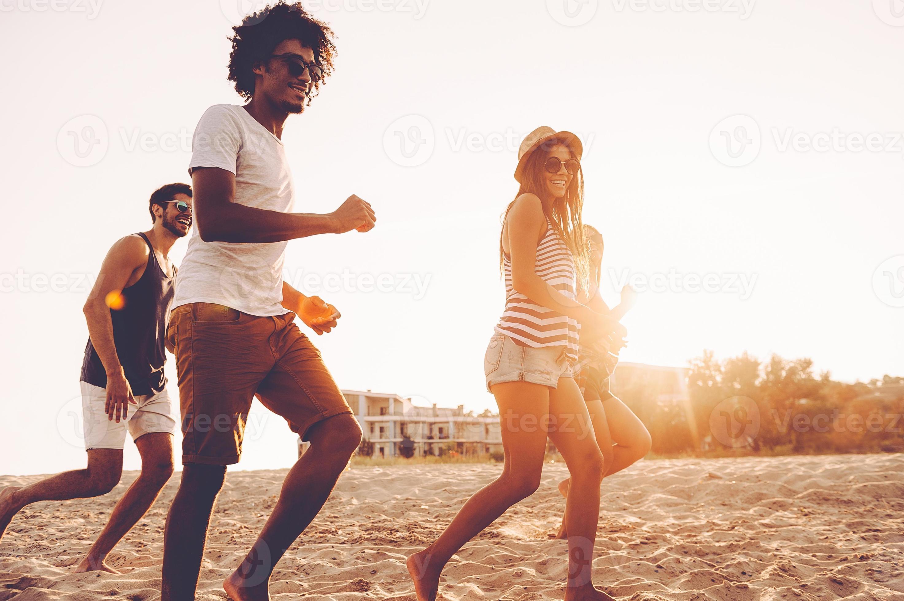 Just keep running Group of young cheerful people running along the beach and looking happy ...