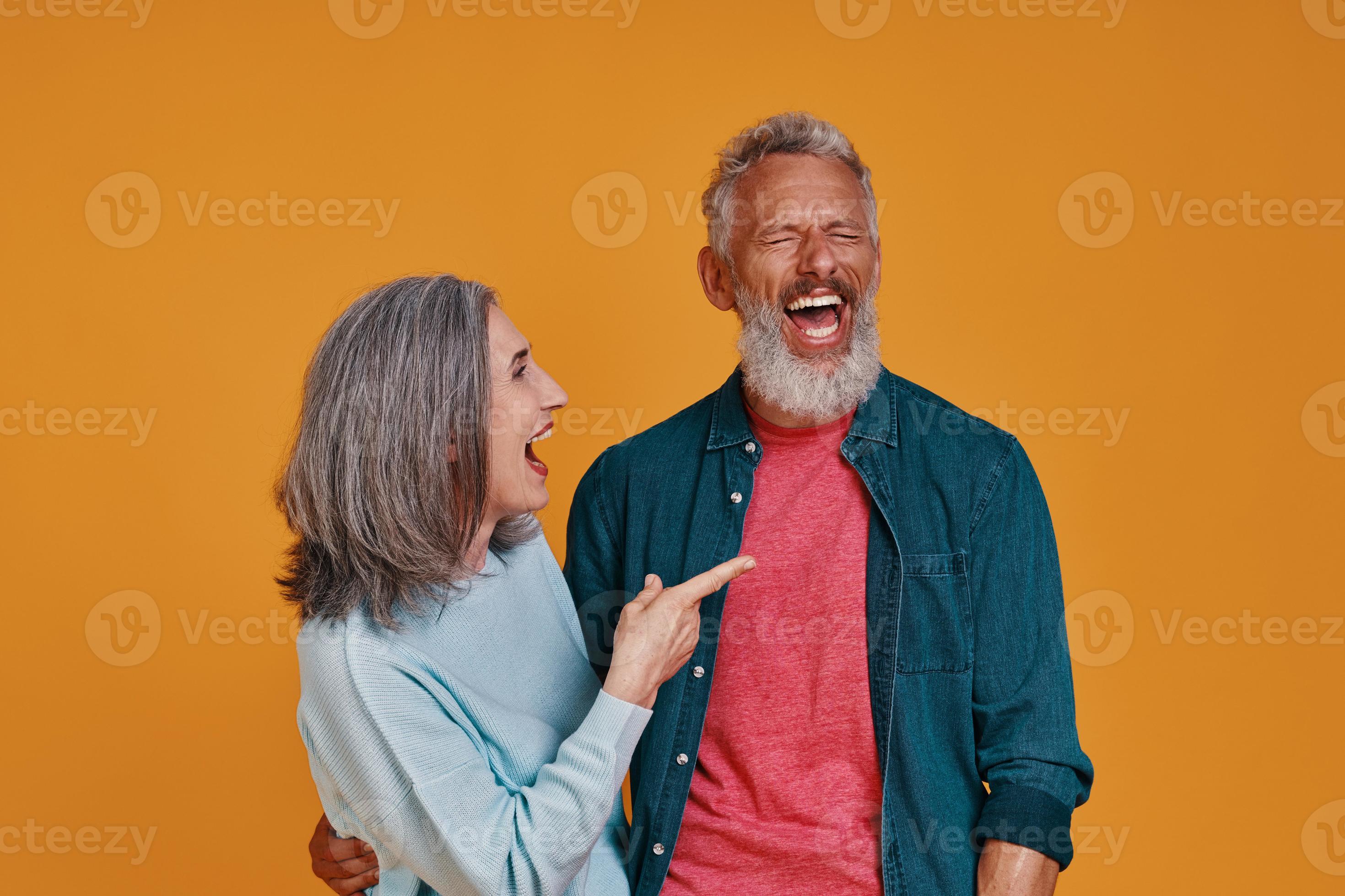 Beautiful Senior Couple Laughing While Standing Together Against Orange