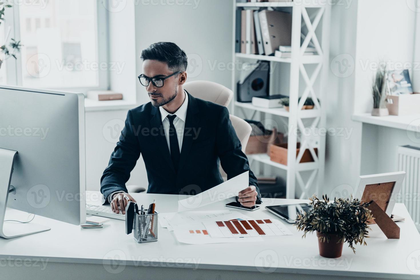 Busy at work. Handsome young man in full suit working with documents ...