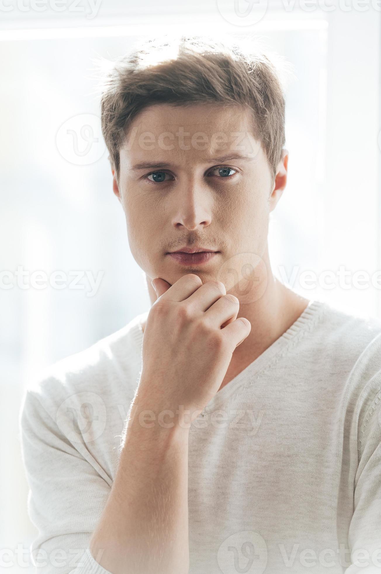 Confident look. Confident young man holding hand on chin and looking at ...
