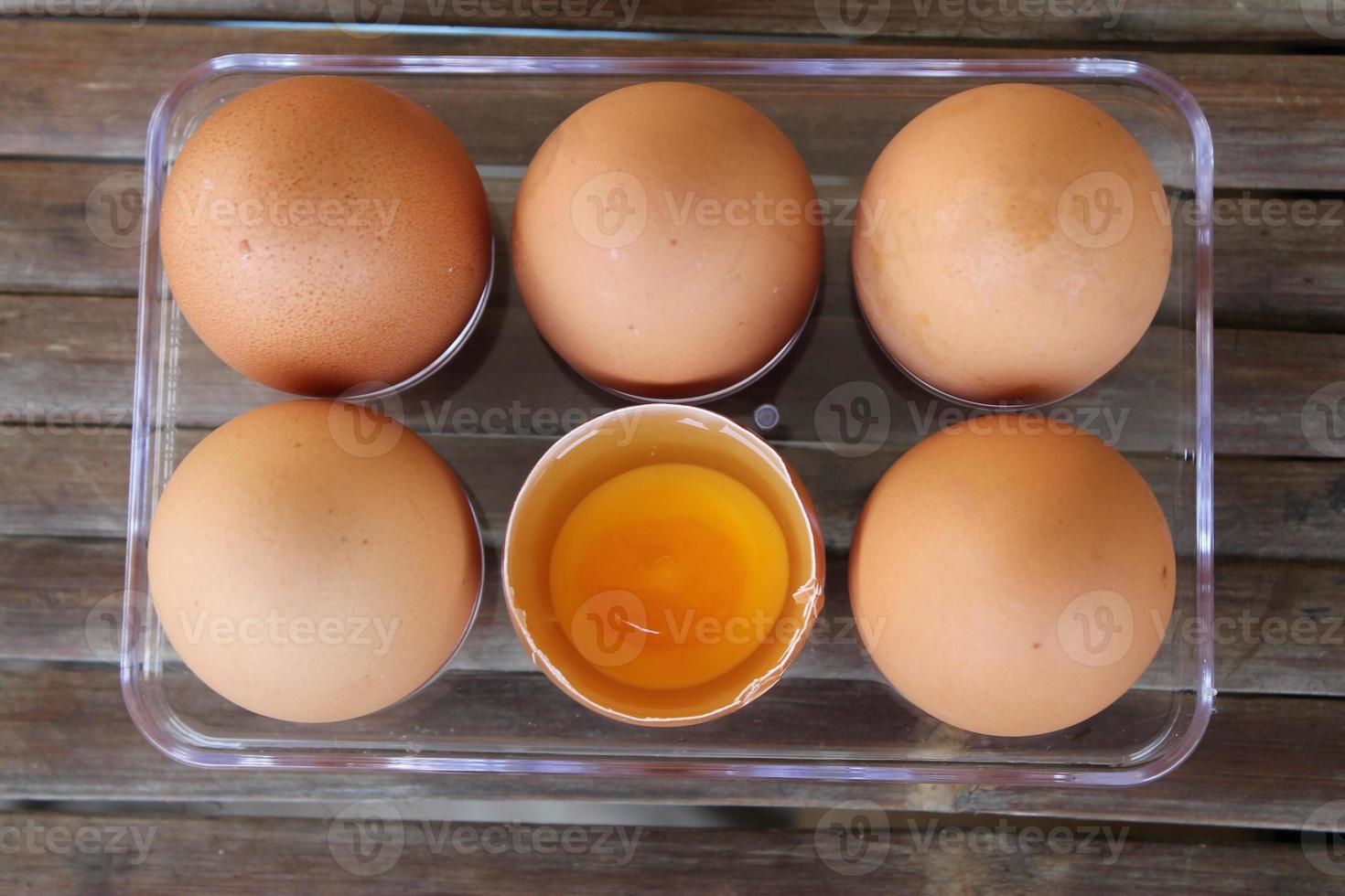 close up Six brown eggs in plastic box on bamboo table with one broken egg, top view. 13685529 ...