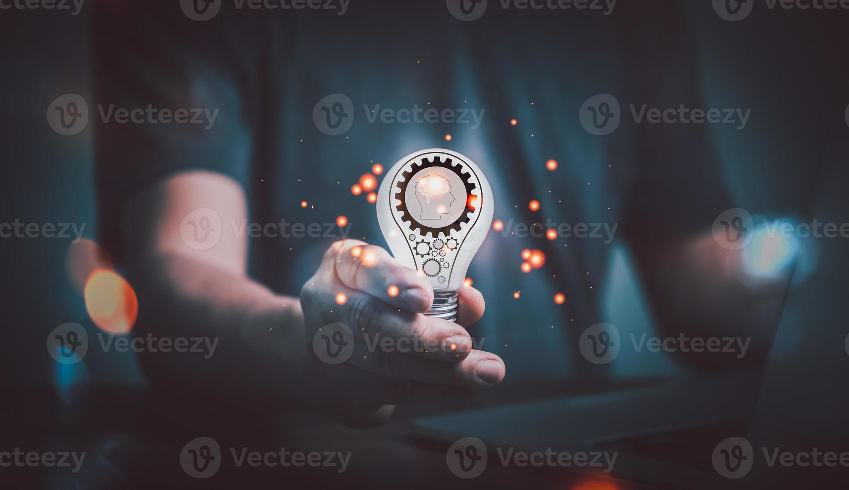 Man hand using computer and holding light bulb with a gear and brain icon in it , The idea of ...