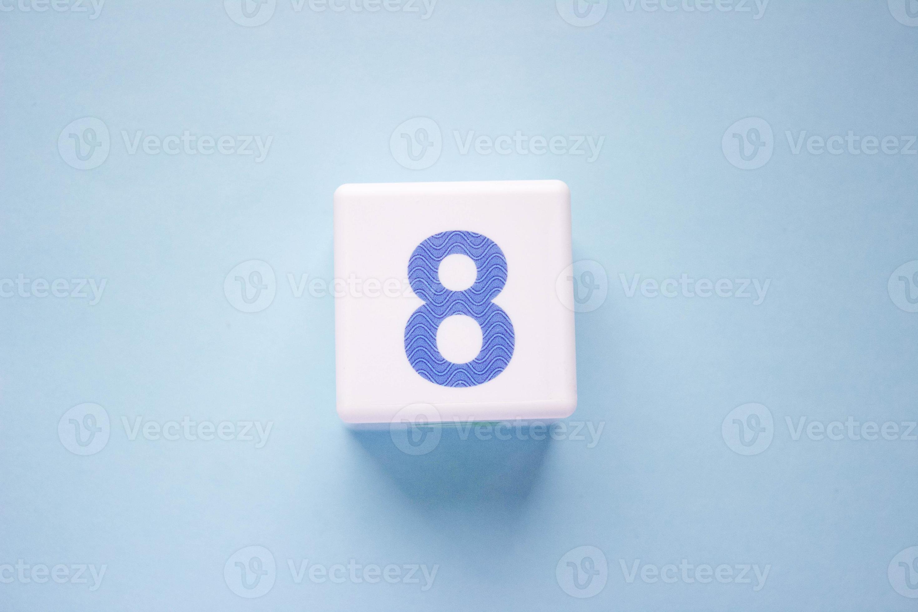 Close-up photo of a white plastic cube with a blue number 8 on a blue background. Object in the ...