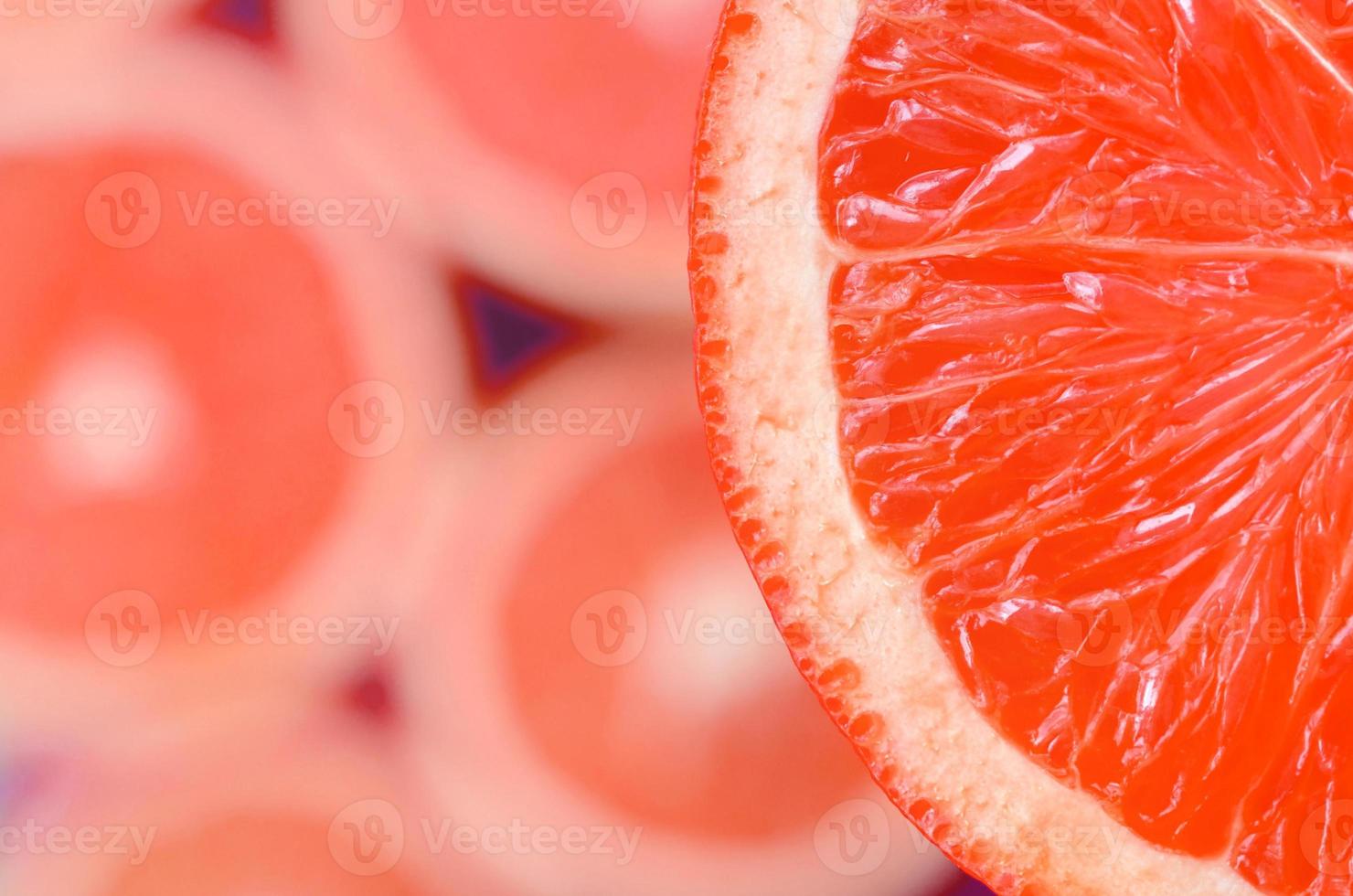 Top view of a fragment of the red grapefruit slice on the background of many blurred grapefruit ...