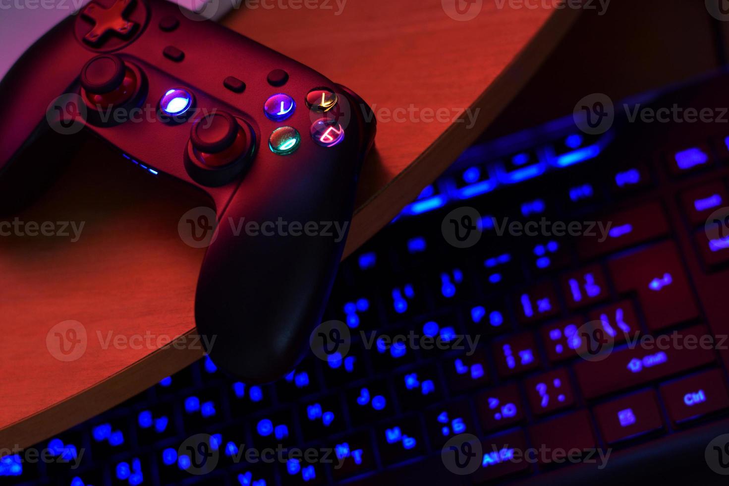 Modern gamepad lies with pc keyboard on table in dark playroom scene. Video game speedrun ...