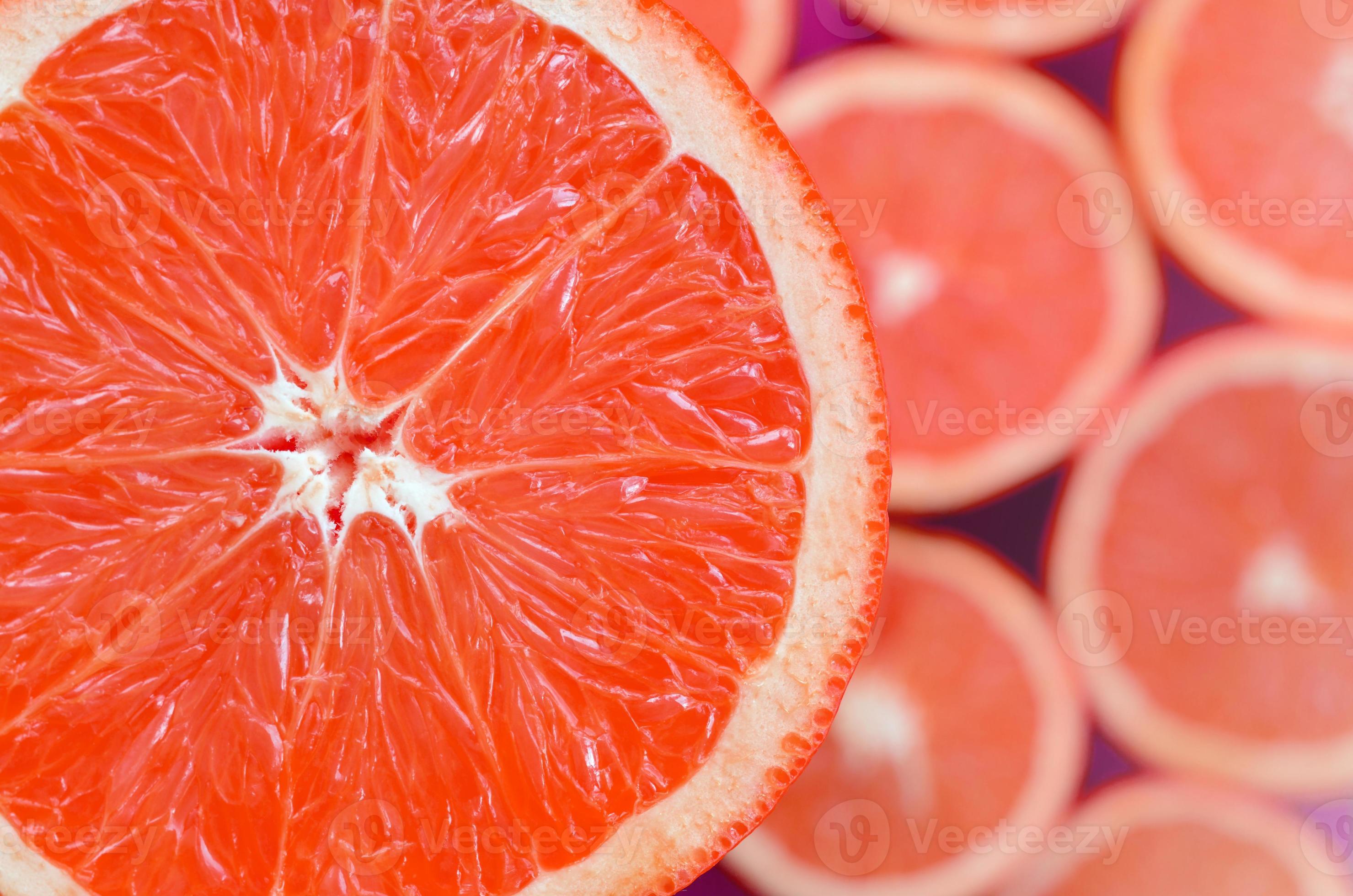 Top view of a fragment of the red grapefruit slice on the background of many blurred grapefruit ...