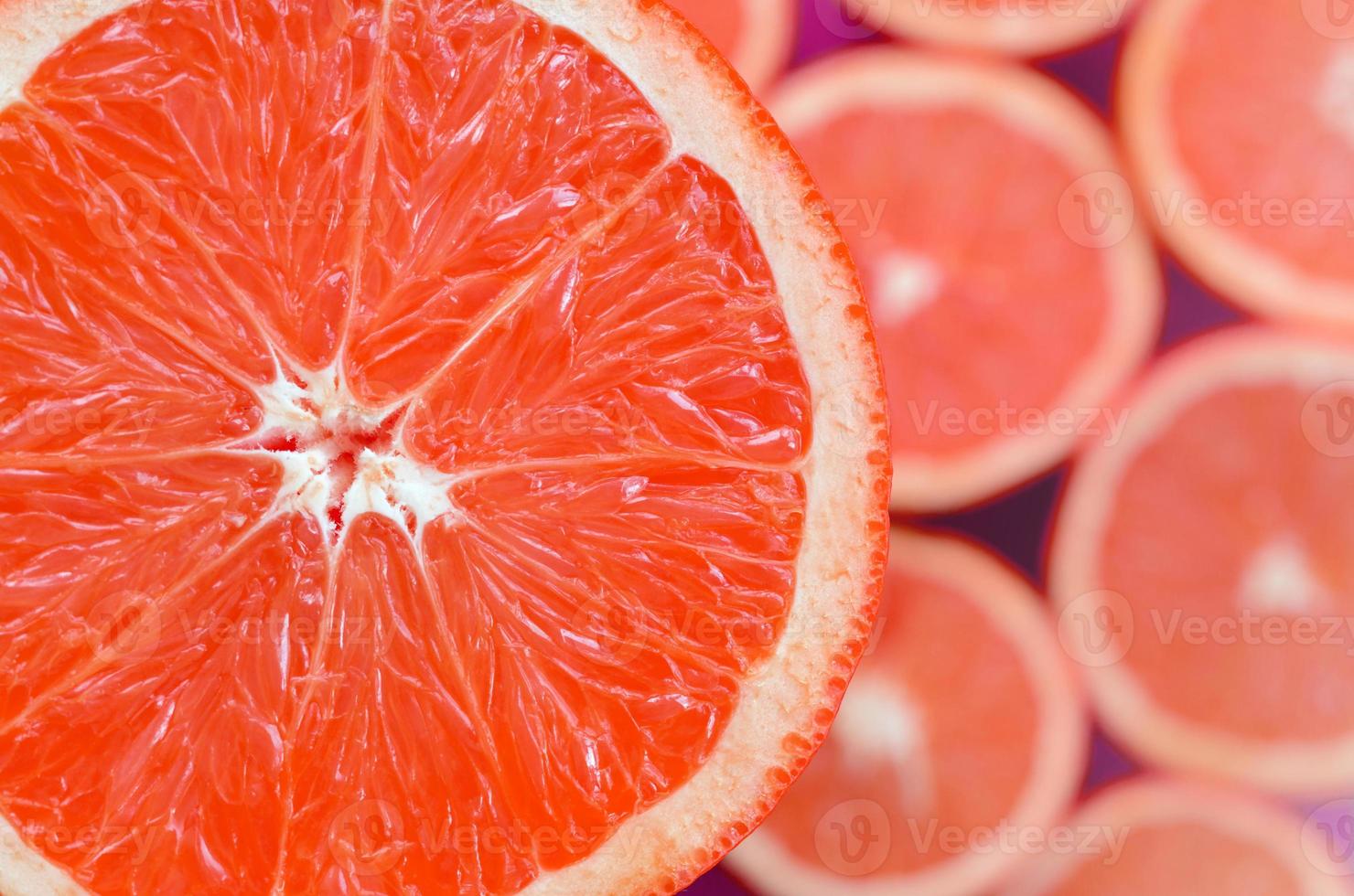 Top view of a fragment of the red grapefruit slice on the background of many blurred grapefruit ...