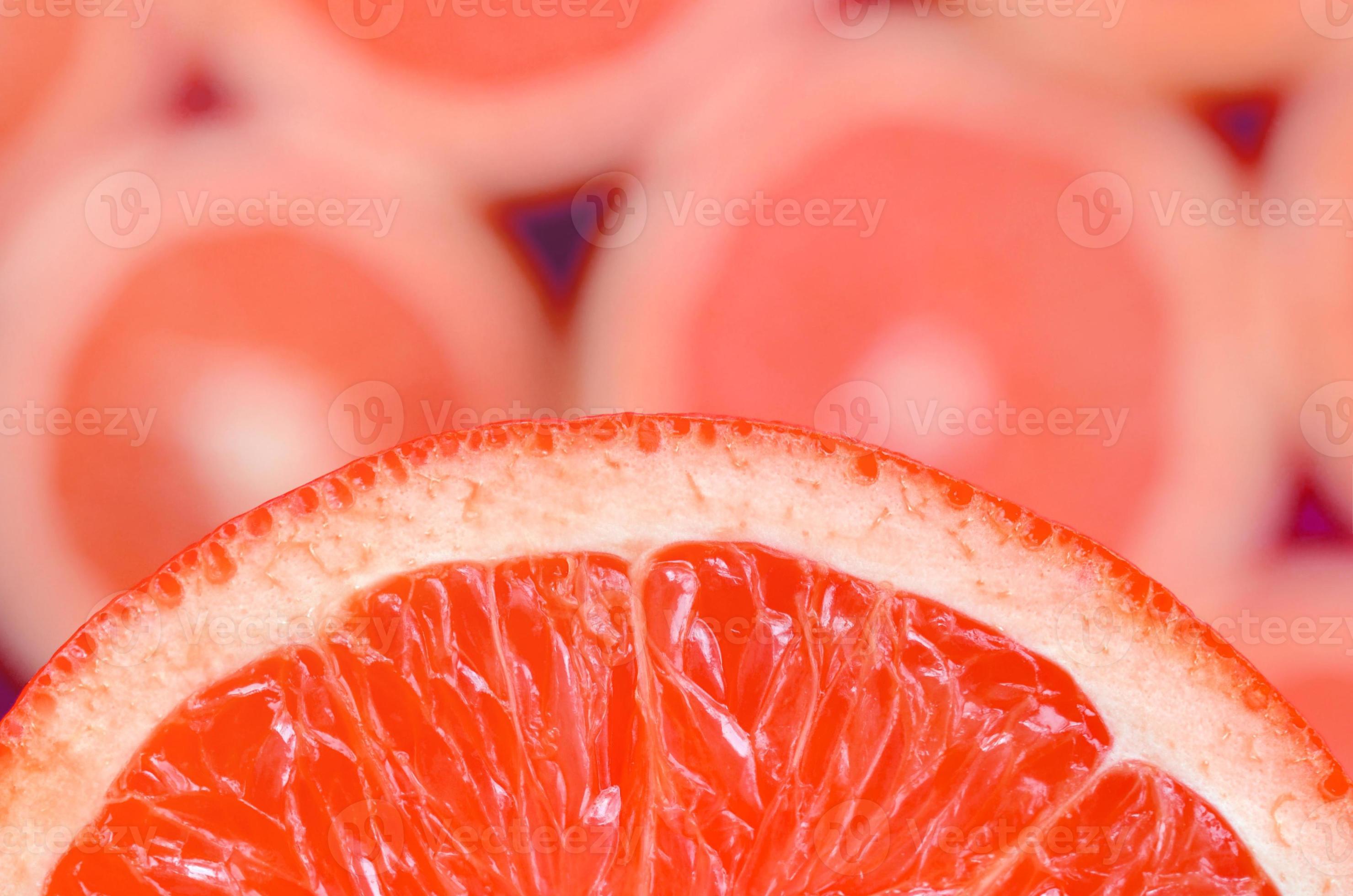 Top view of a fragment of the red grapefruit slice on the background of many blurred grapefruit ...