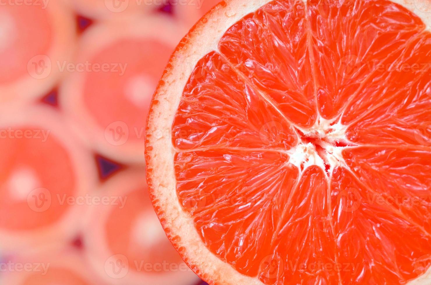 Top view of a fragment of the red grapefruit slice on the background of many blurred grapefruit ...