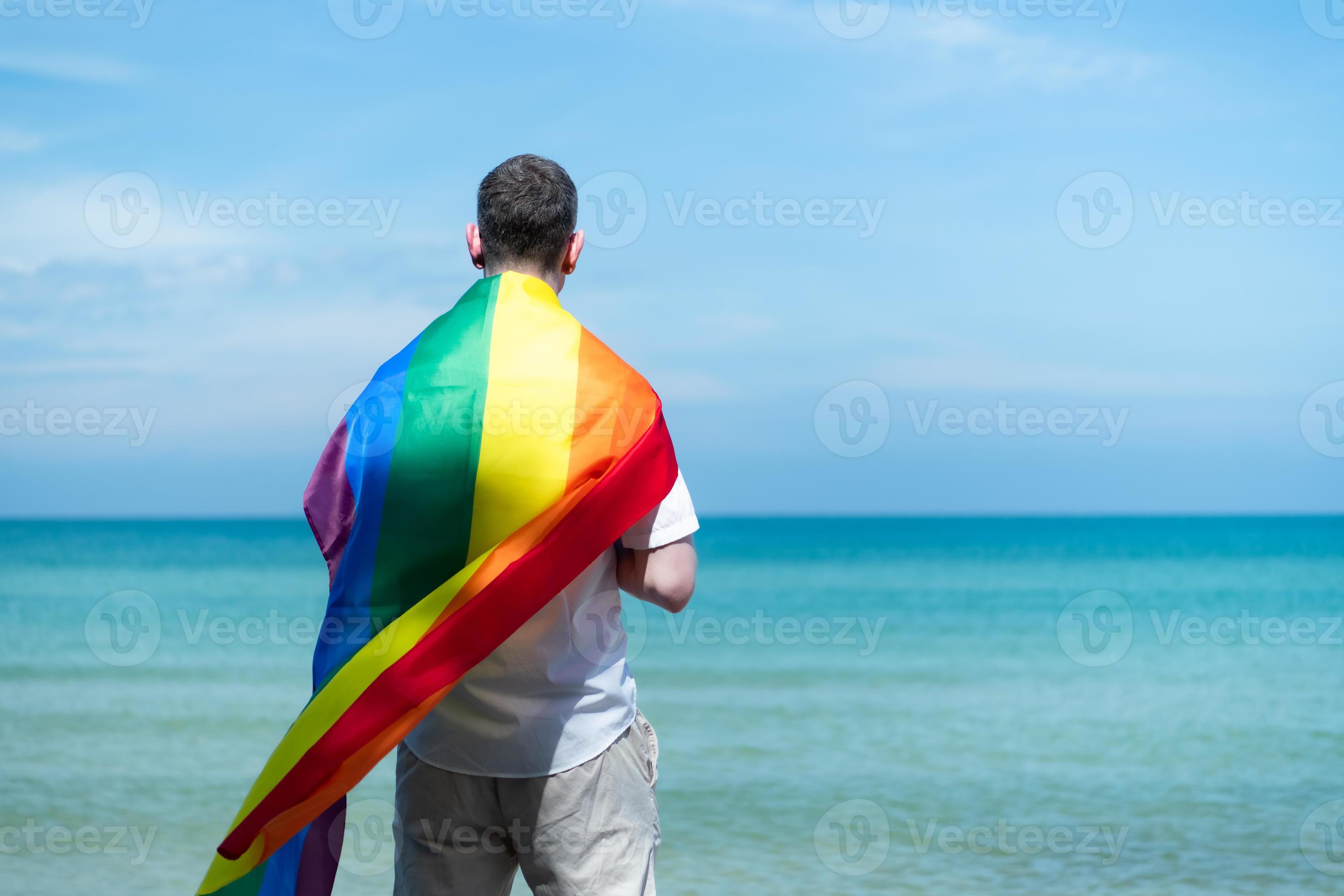 Young Gay Man Holding Rainbow Flags While Standing On The Beach
